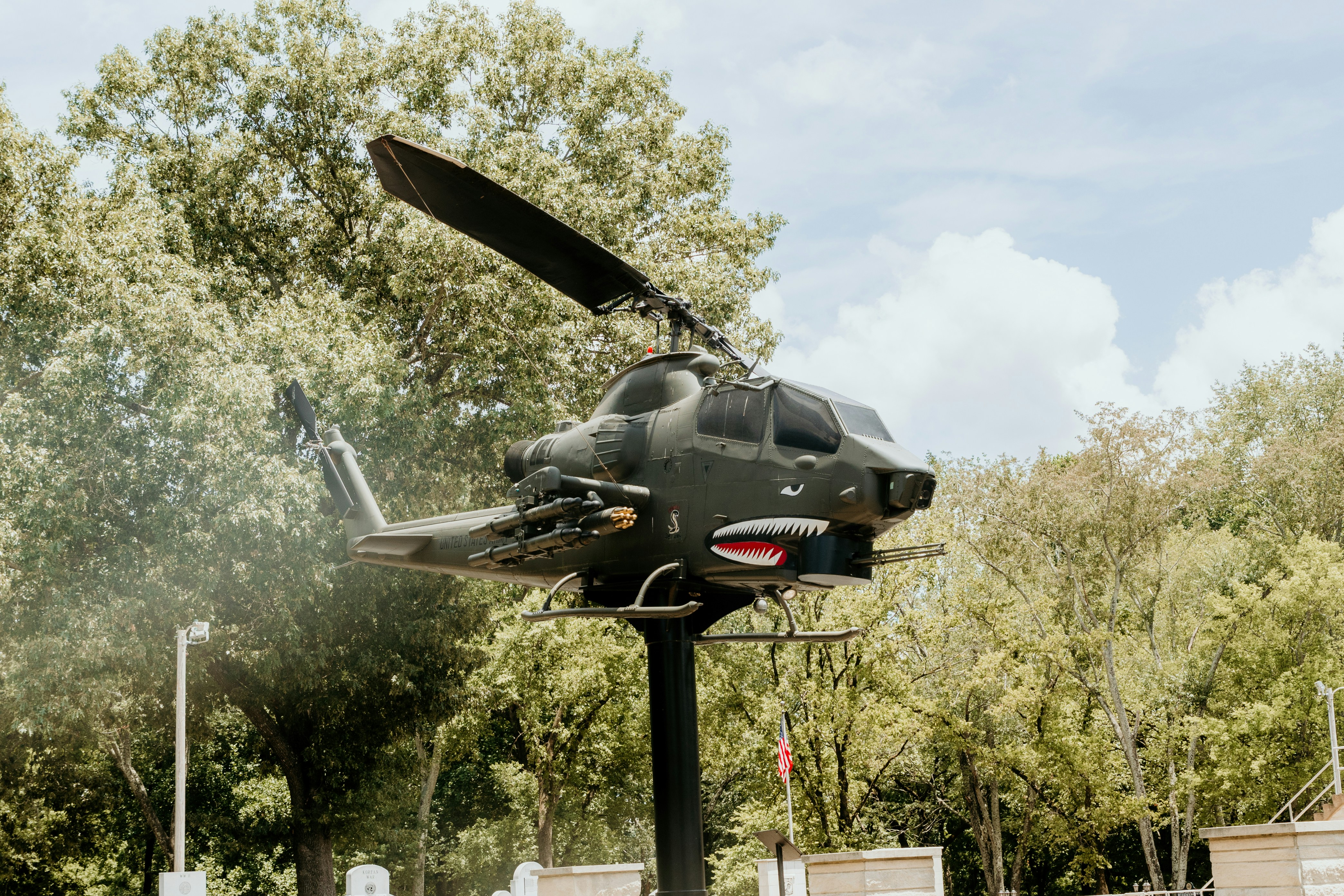 Shark-mouthed Sentinel: A Static Helicopter on a Pedestal in Dappled Light