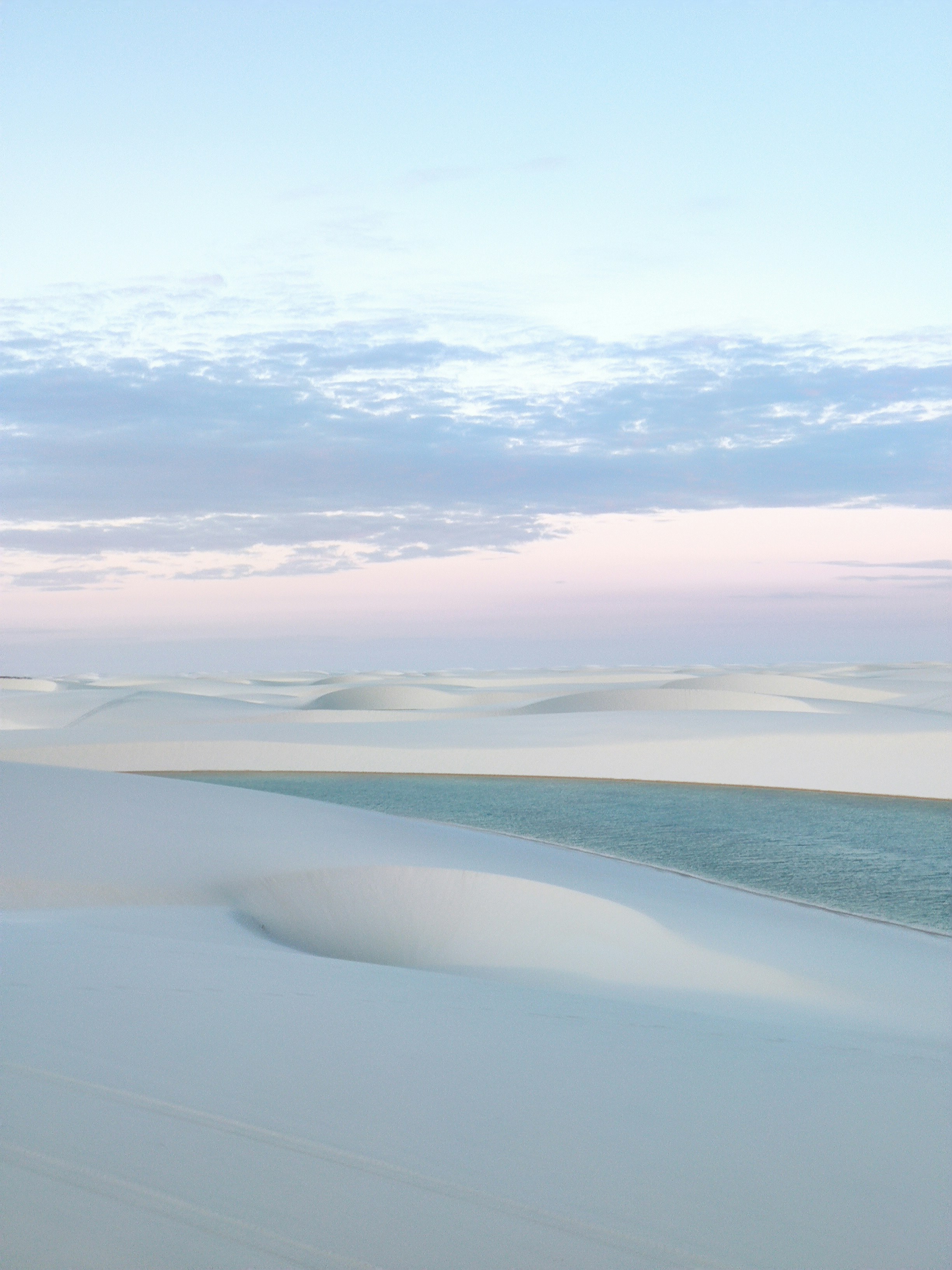 Gentle undulating sand dunes meet a tranquil lagoon under a pastel sky. The scene embodies the quiet beauty of nature's contrasts.
