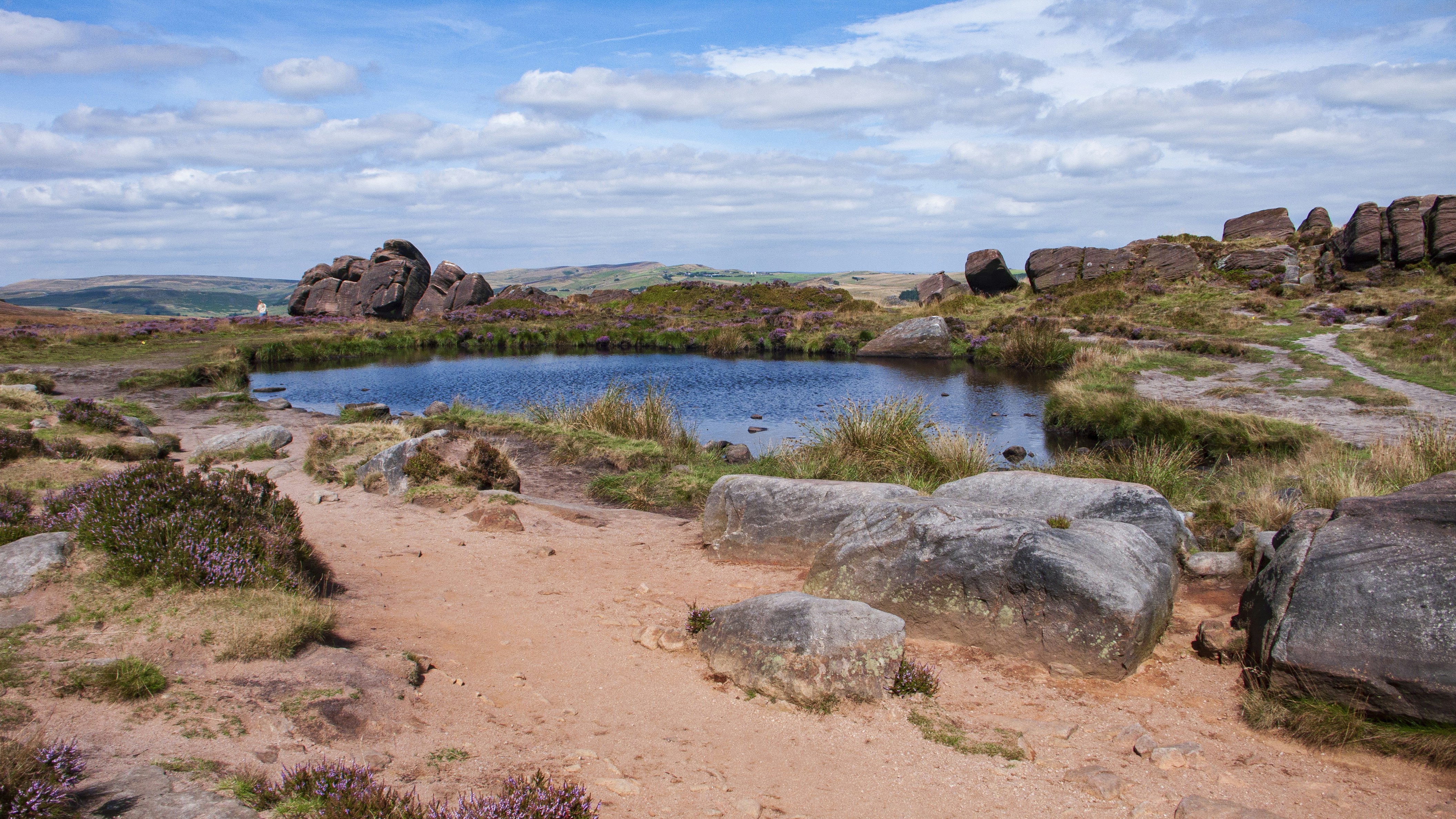 Tranquil pool surrounded by rugged rocks under a bright sky on the Peak District moorlands.