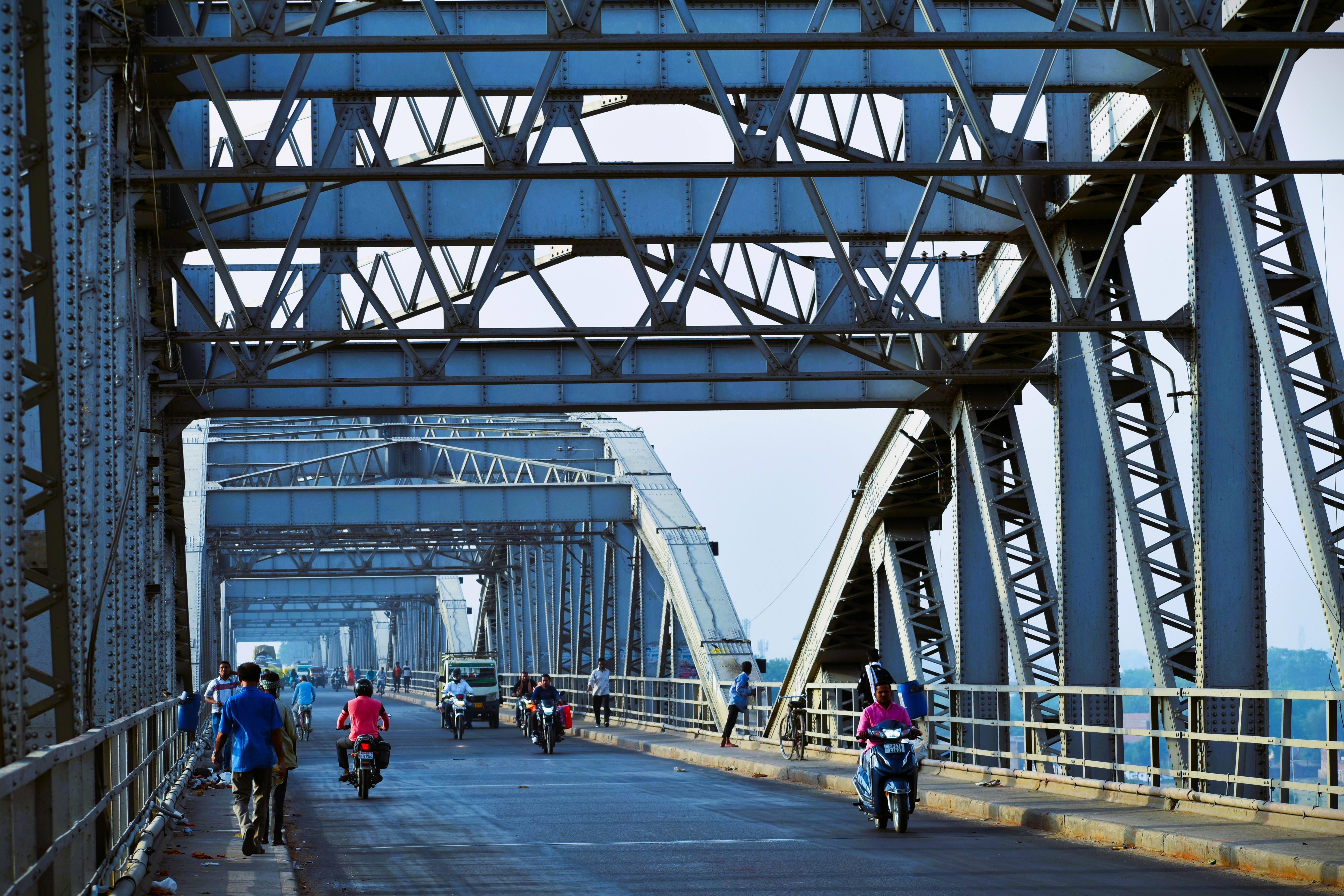 Motorcycles and pedestrians traverse a steel bridge, showcasing the intricate architecture and daily movement of urban life.
