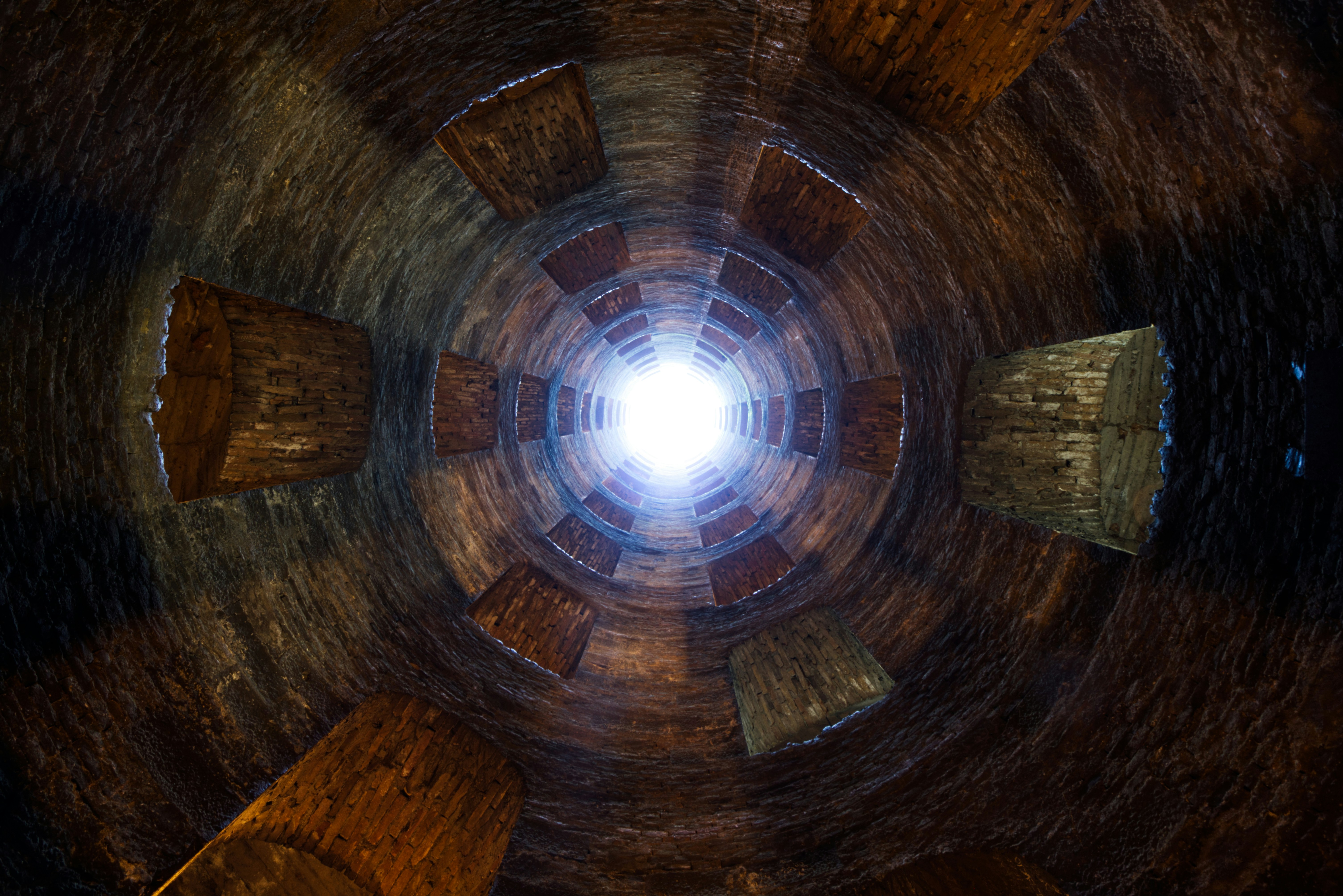 View from inside a cylindrical stone tower, with a bright light at the top illuminating the textured walls.