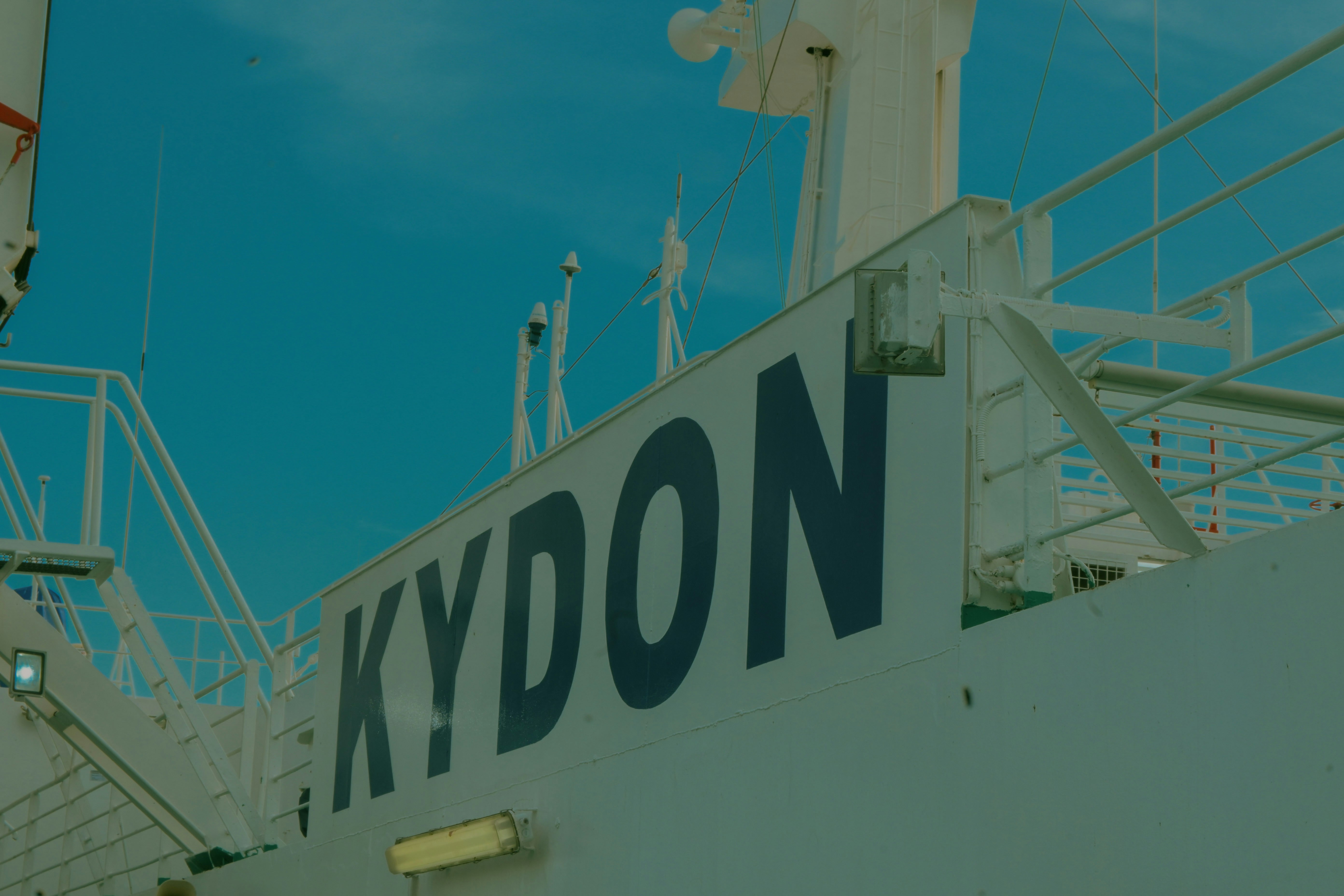 White ship with bold lettering 'KYDON' set against a teal sky.