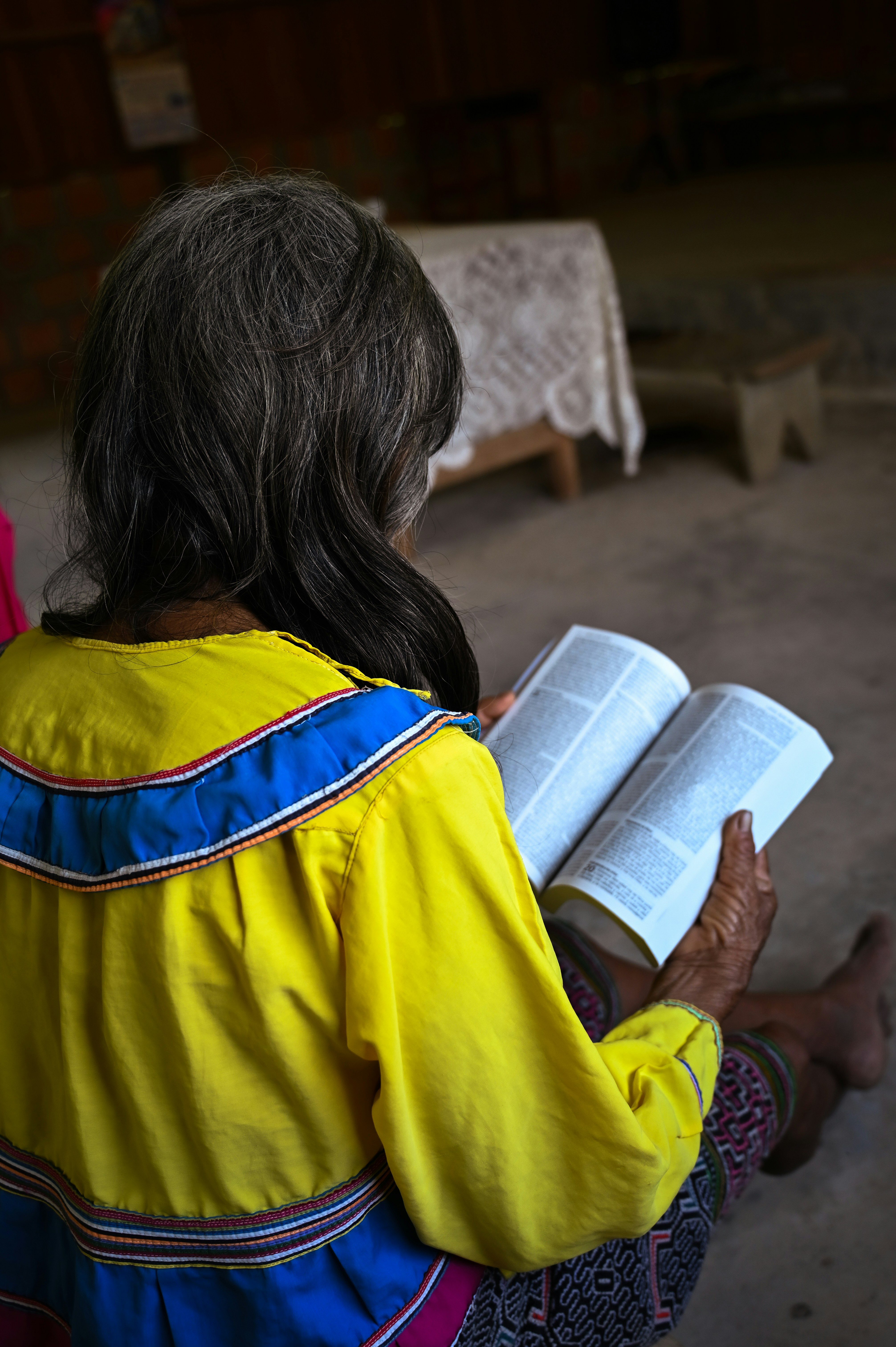 Elderly woman in traditional attire engrossed in a book, showcasing cultural heritage and the pursuit of knowledge.