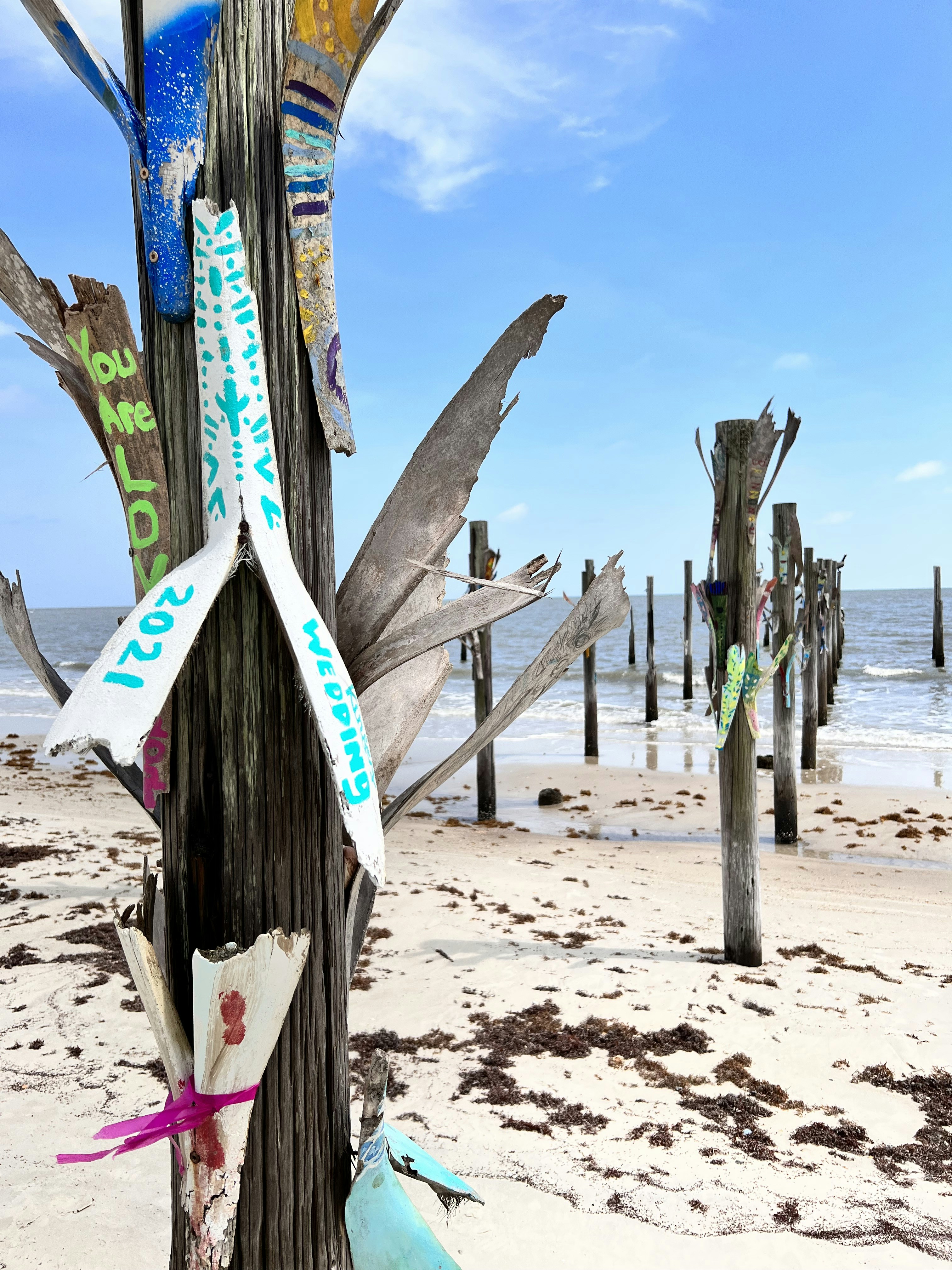 Sea-stained Totem: Painted Driftwood Markers Rise from Sandy Shore