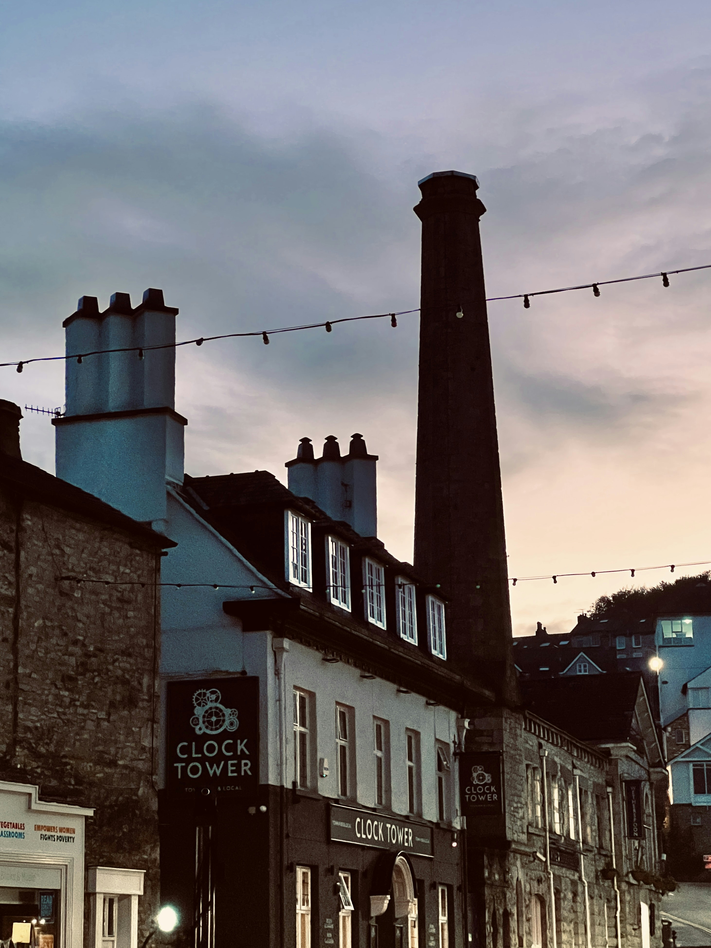 Dusk Over the Clock Tower Street: A Tall Brick Chimney Frames the Historic Inn Row
