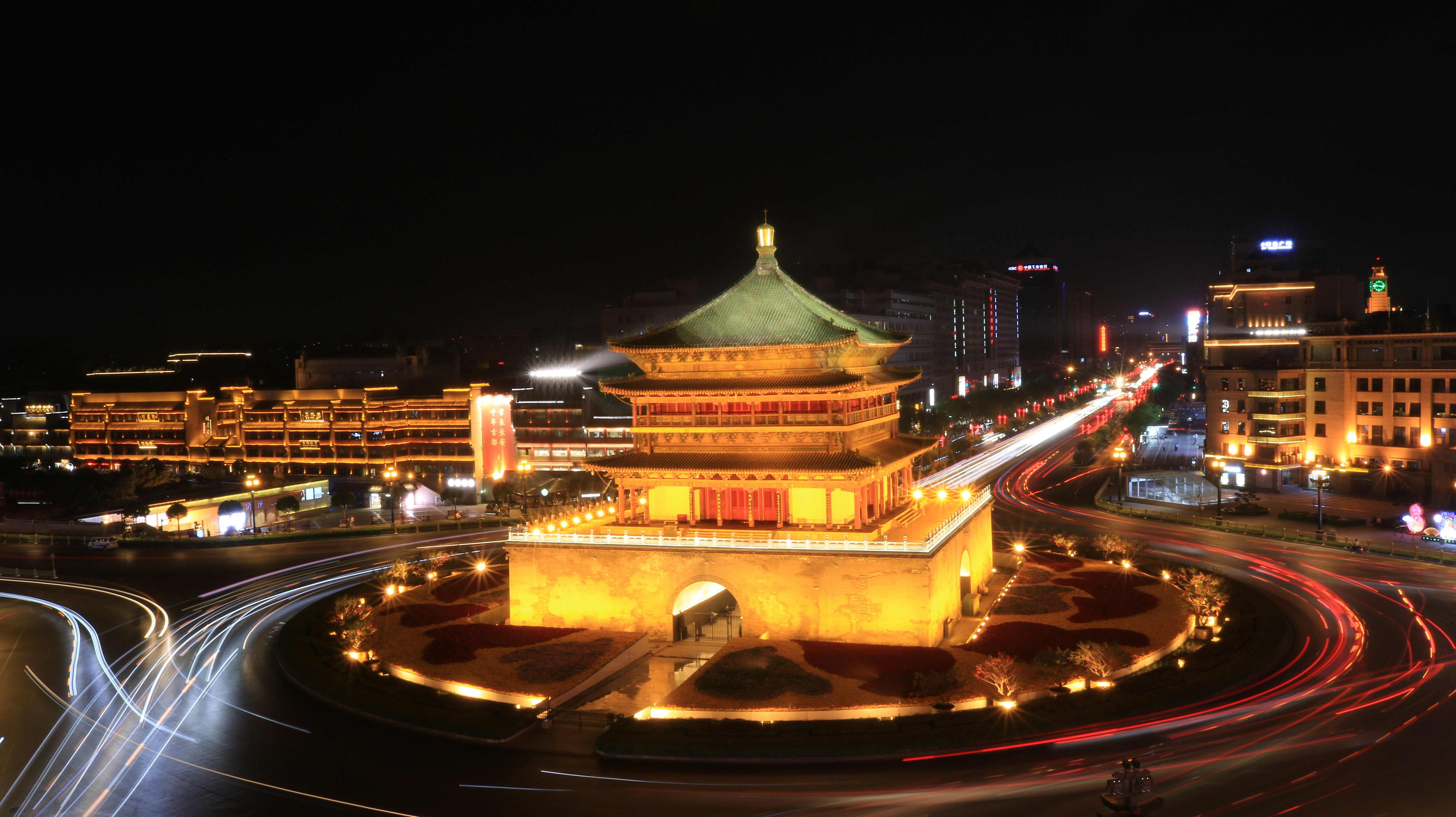 Historic bell tower glowing with golden lights in a bustling urban nightscape.
