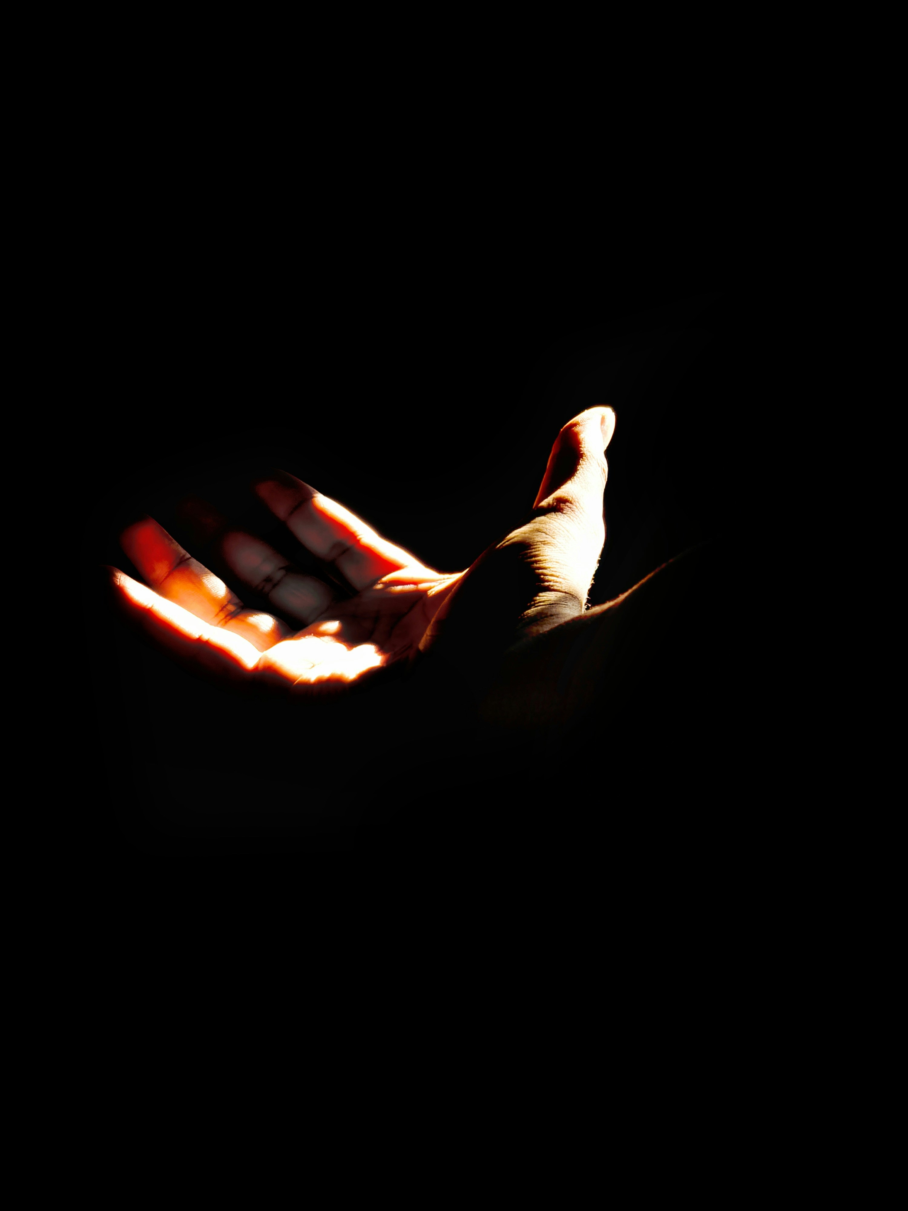 A hand reaching out, partially illuminated against a dark background, symbolizing connection and aspiration.