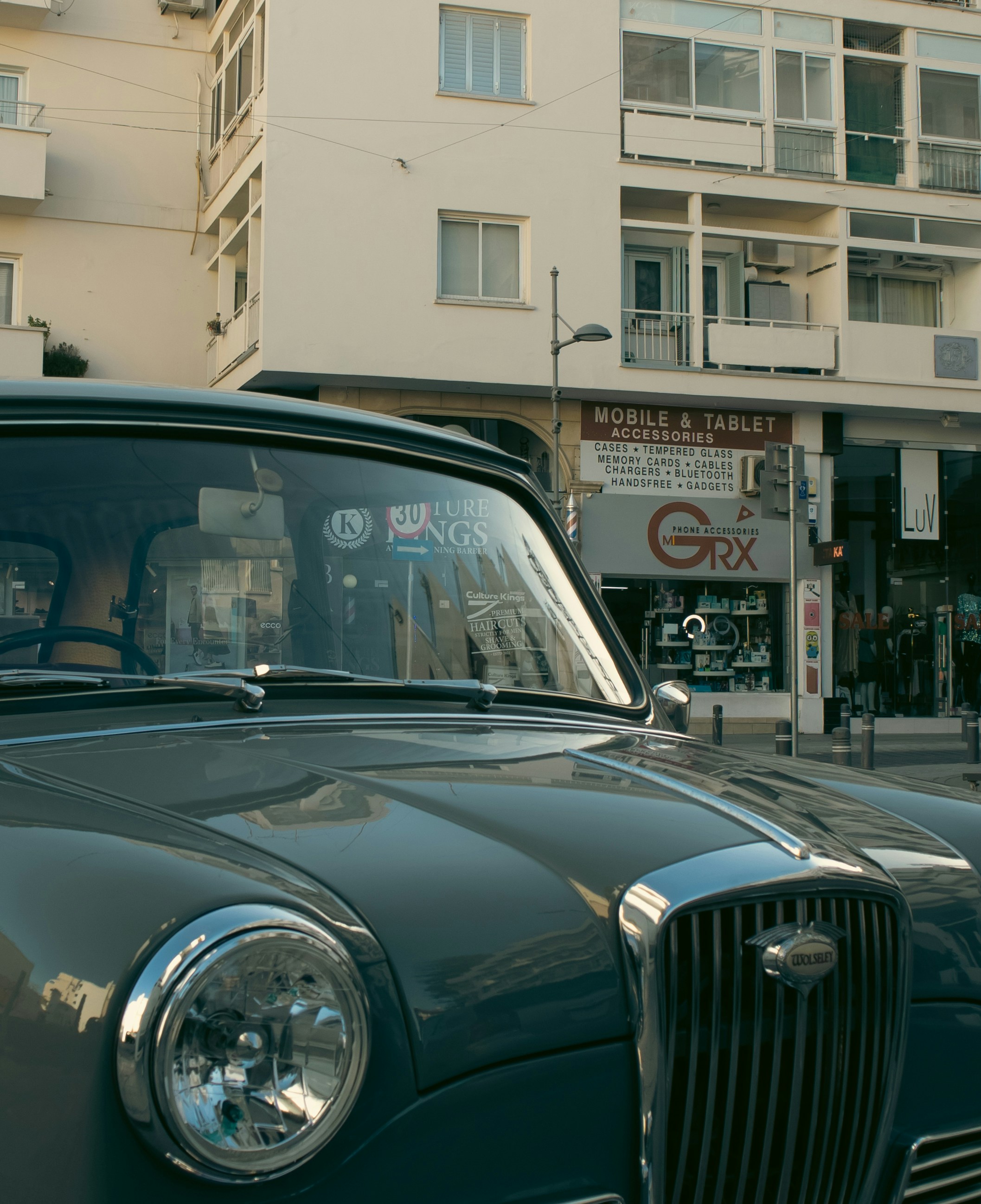 Chrome Grille in Focus: A Vintage Car Framed by Urban Storefronts