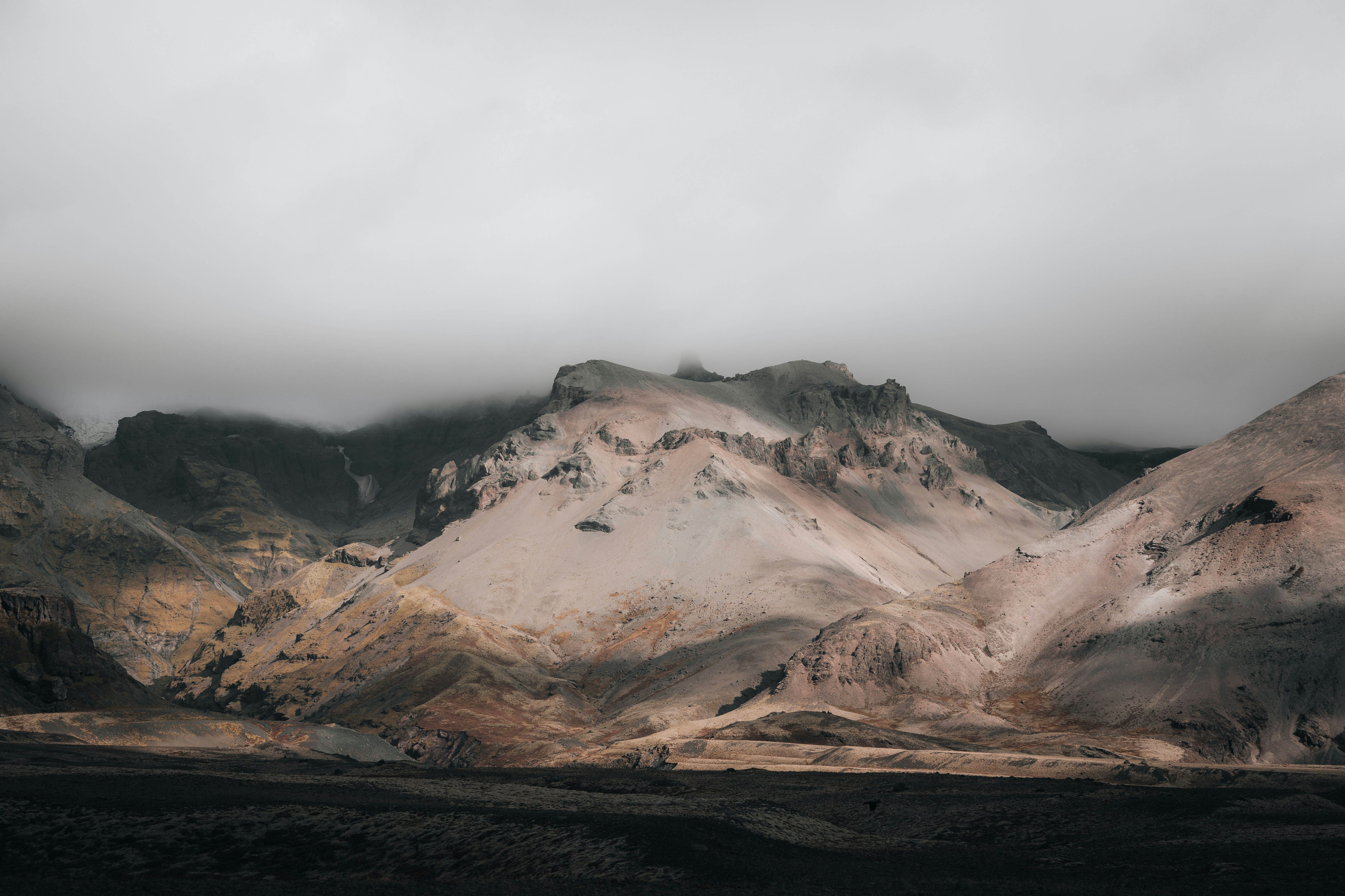 Dramatic mountain landscape shrouded in clouds, showcasing rugged terrain and muted colors. A blend of earth tones highlights the natural beauty of the highlands.