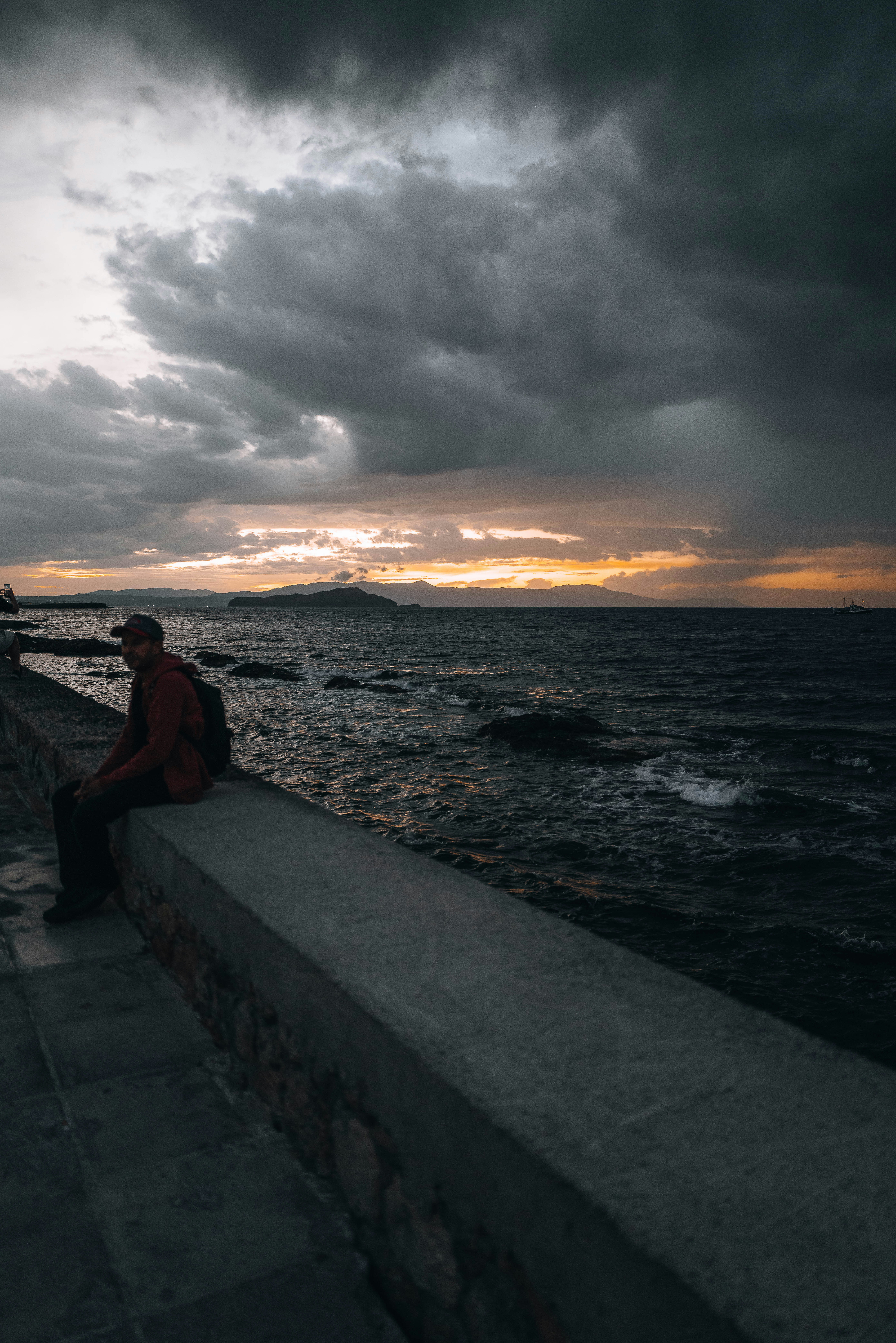 A person sitting on a ledge overlooking the ocean photo – Free Chania ...