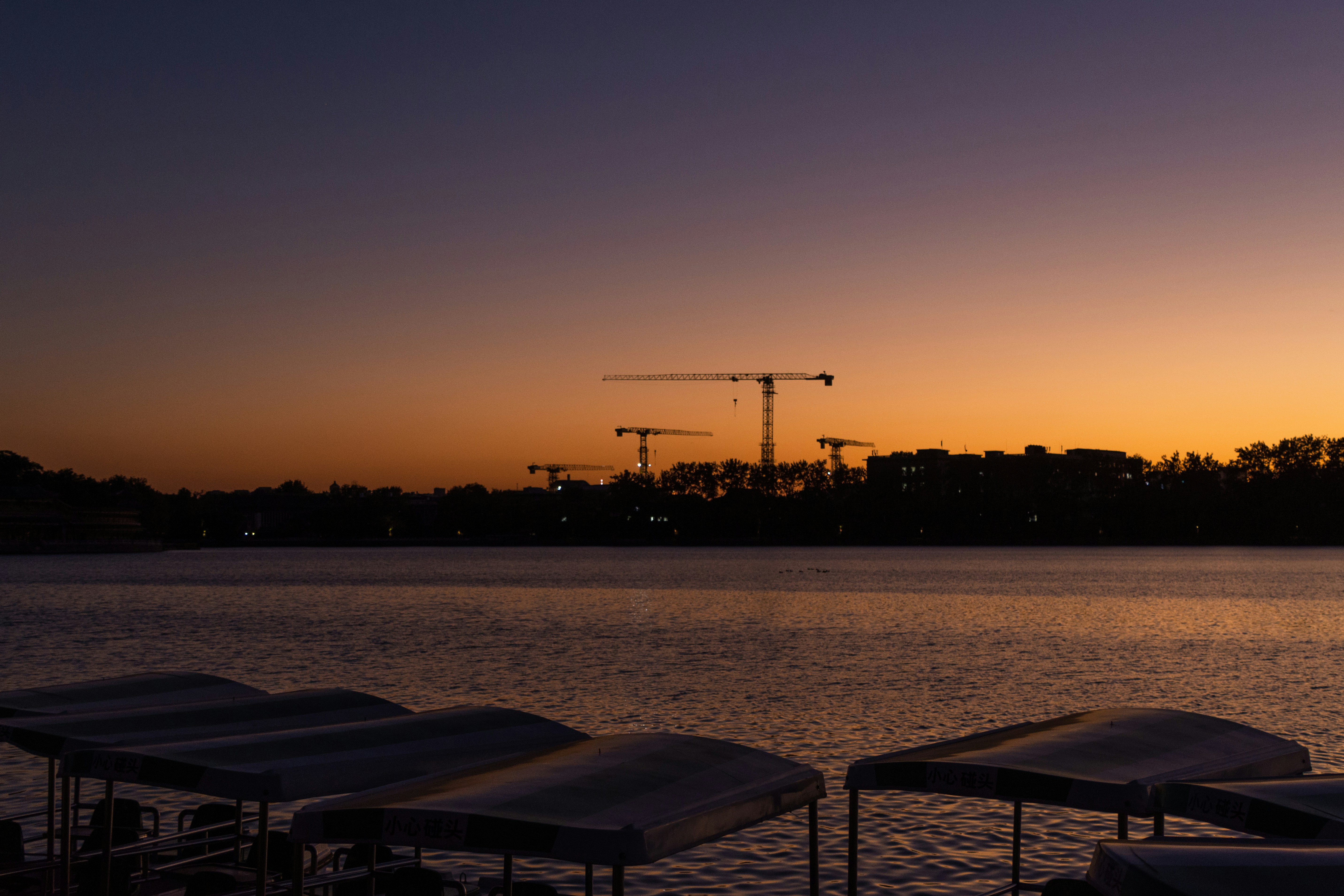 Silhouetted harbor at sunset with distant cranes