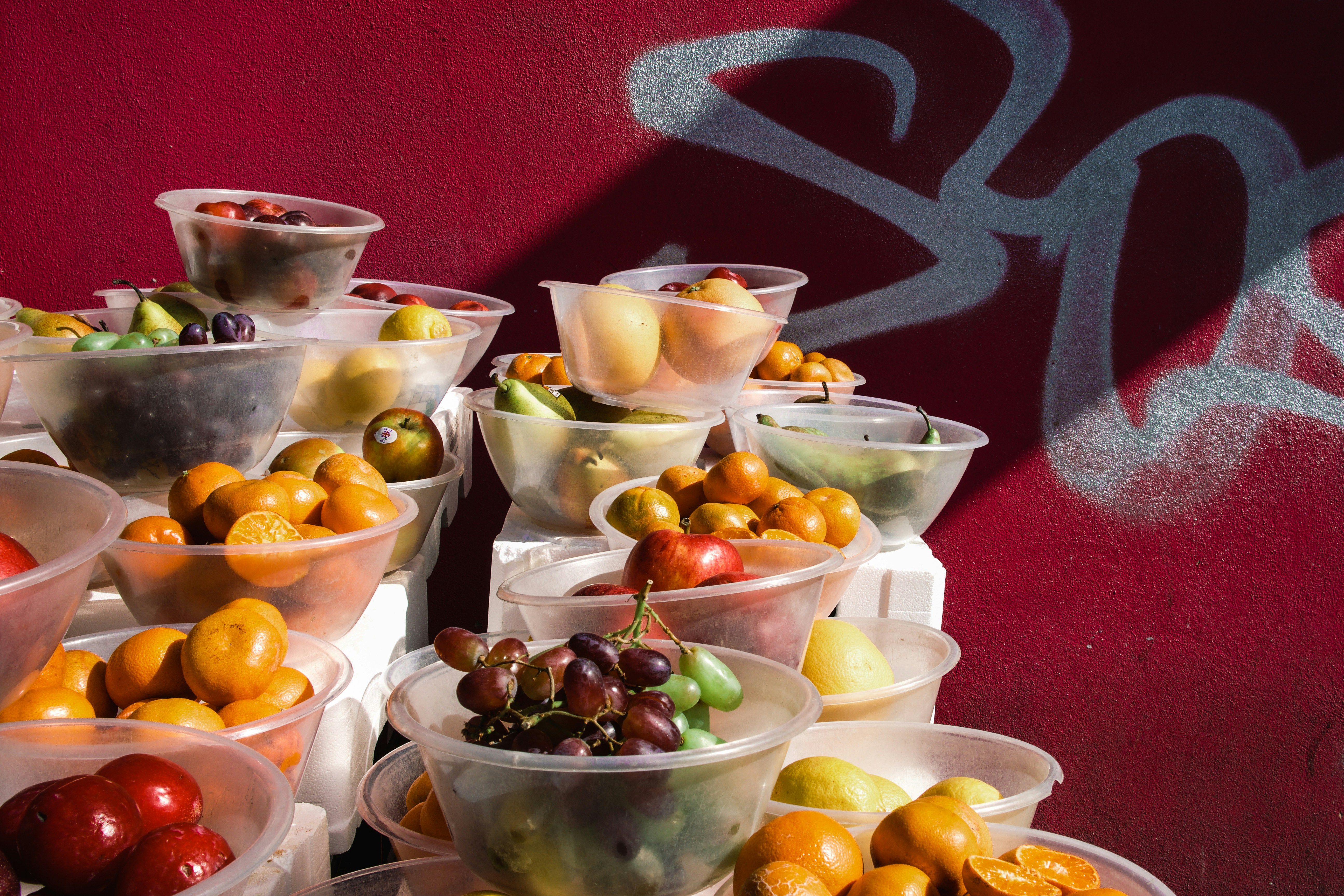 Fruit bowls in a sunlit street stall with a crimson wall backdrop