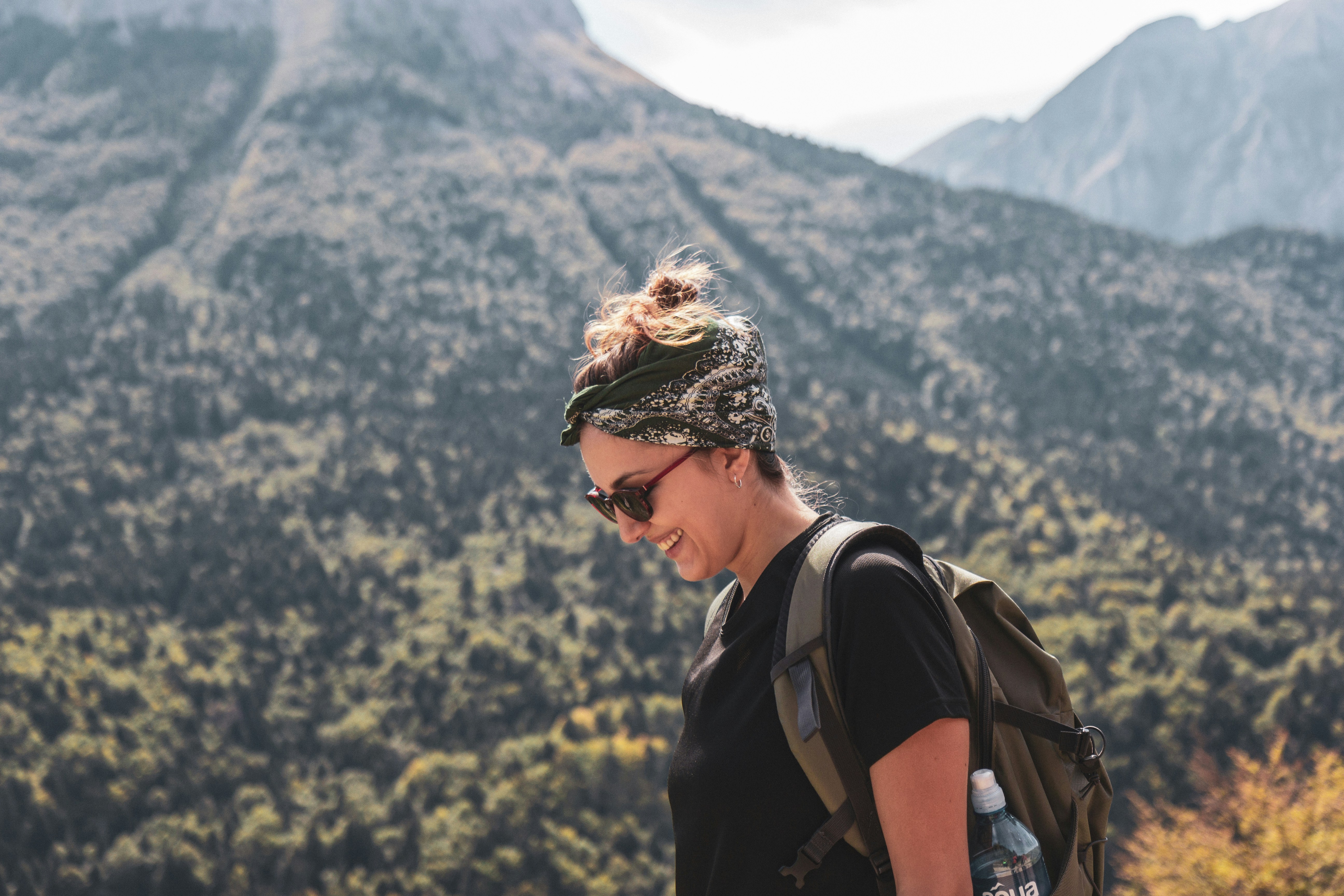 Woman smiling with a backpack against a backdrop of rugged mountains and autumn foliage.