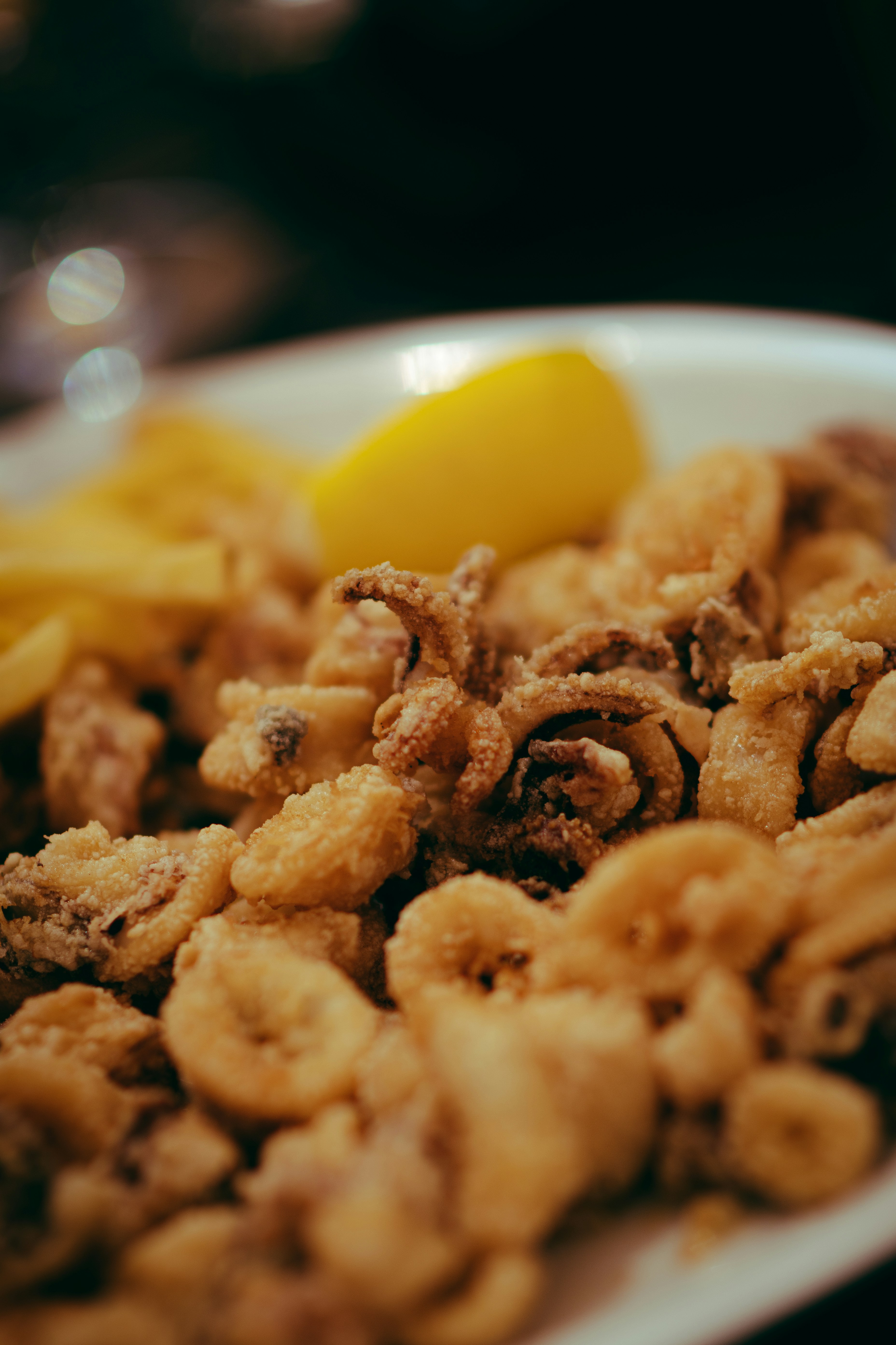 Plate of crispy fried calamari accompanied by a wedge of lemon and golden fries. Perfectly textured and inviting.