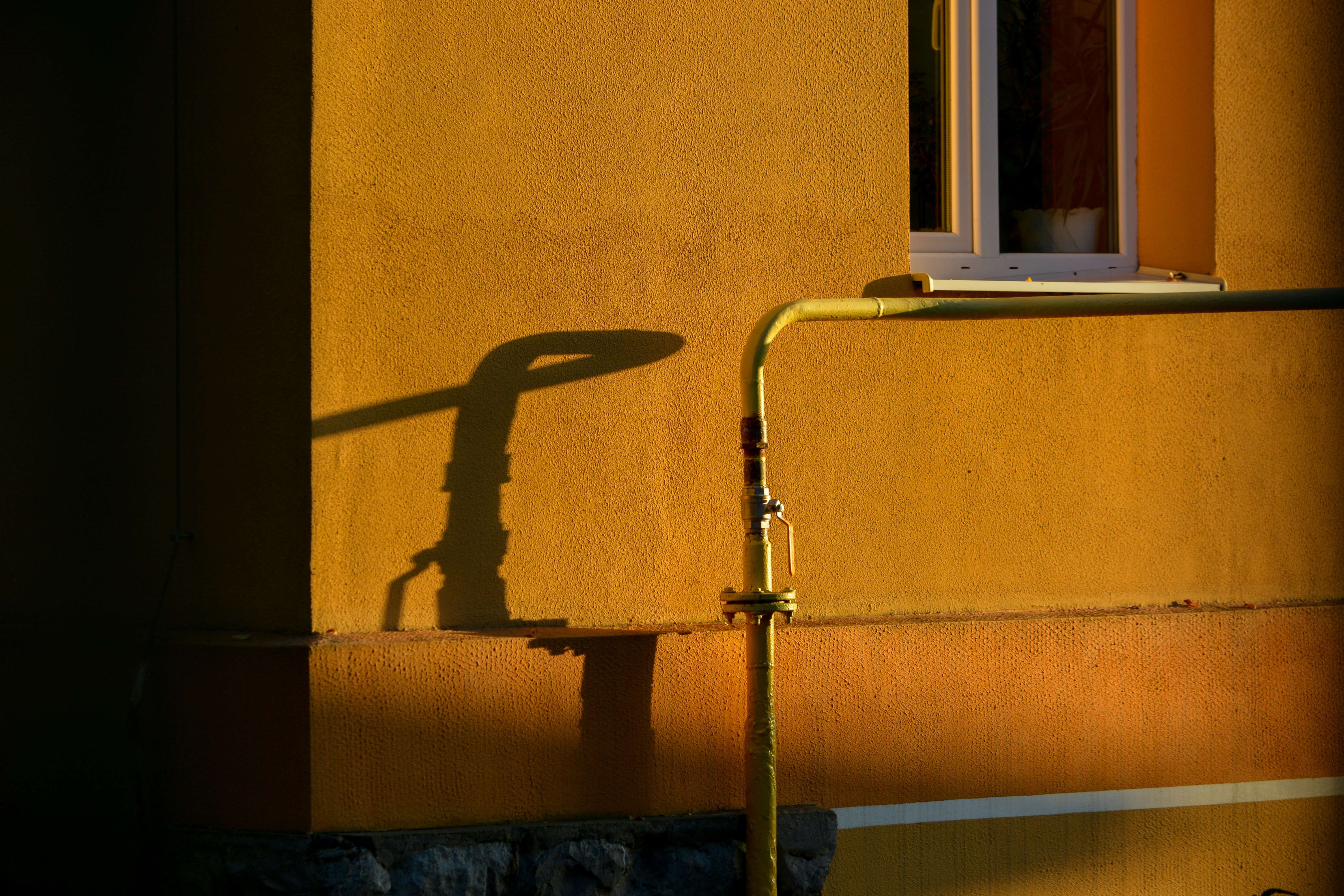 Sunlit Pipe and Shadow on a Golden Wall