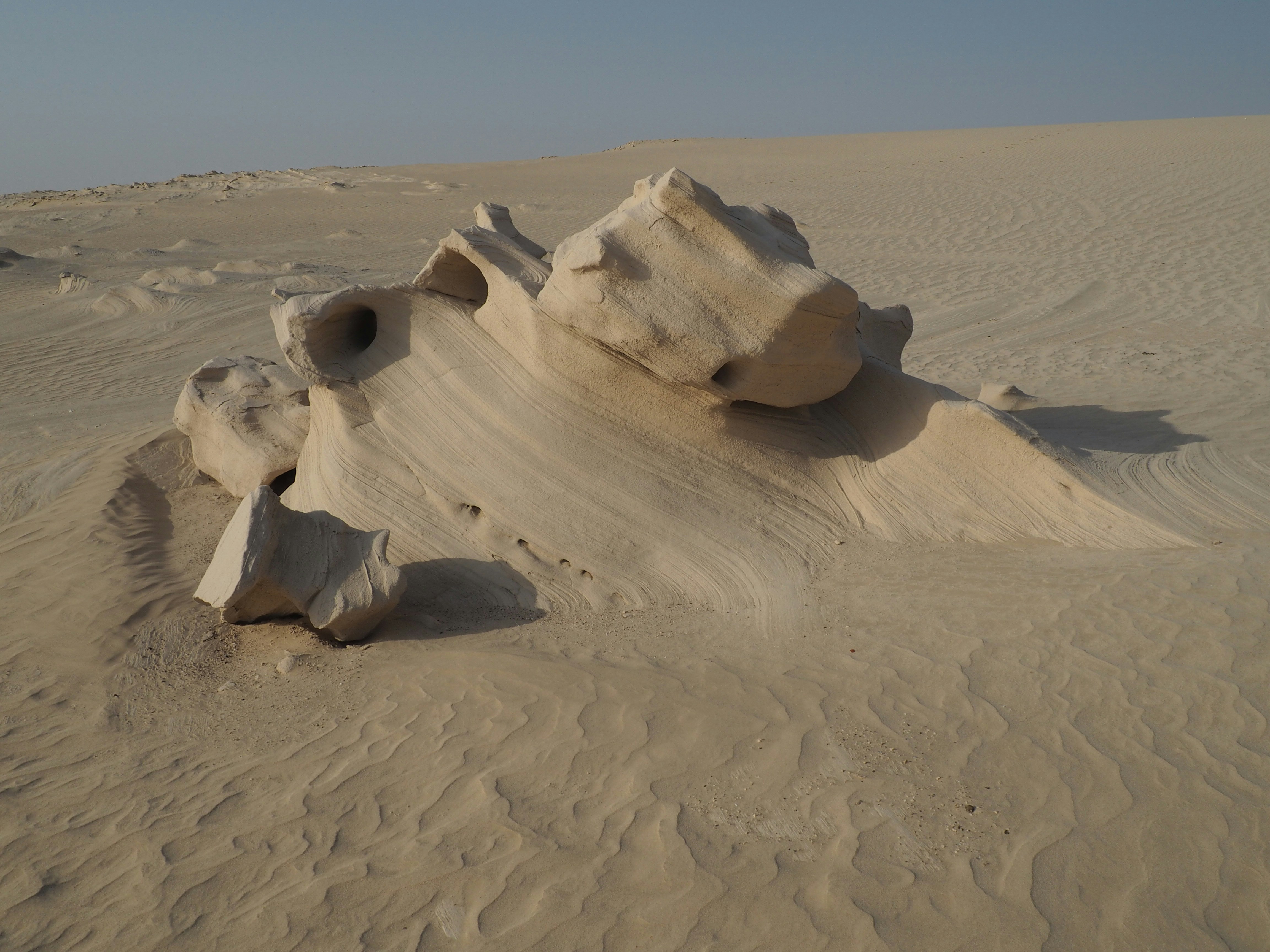 Unique rock formations shaped by wind erosion amidst expansive desert sands. The textures and patterns reveal the natural artistry of the environment.