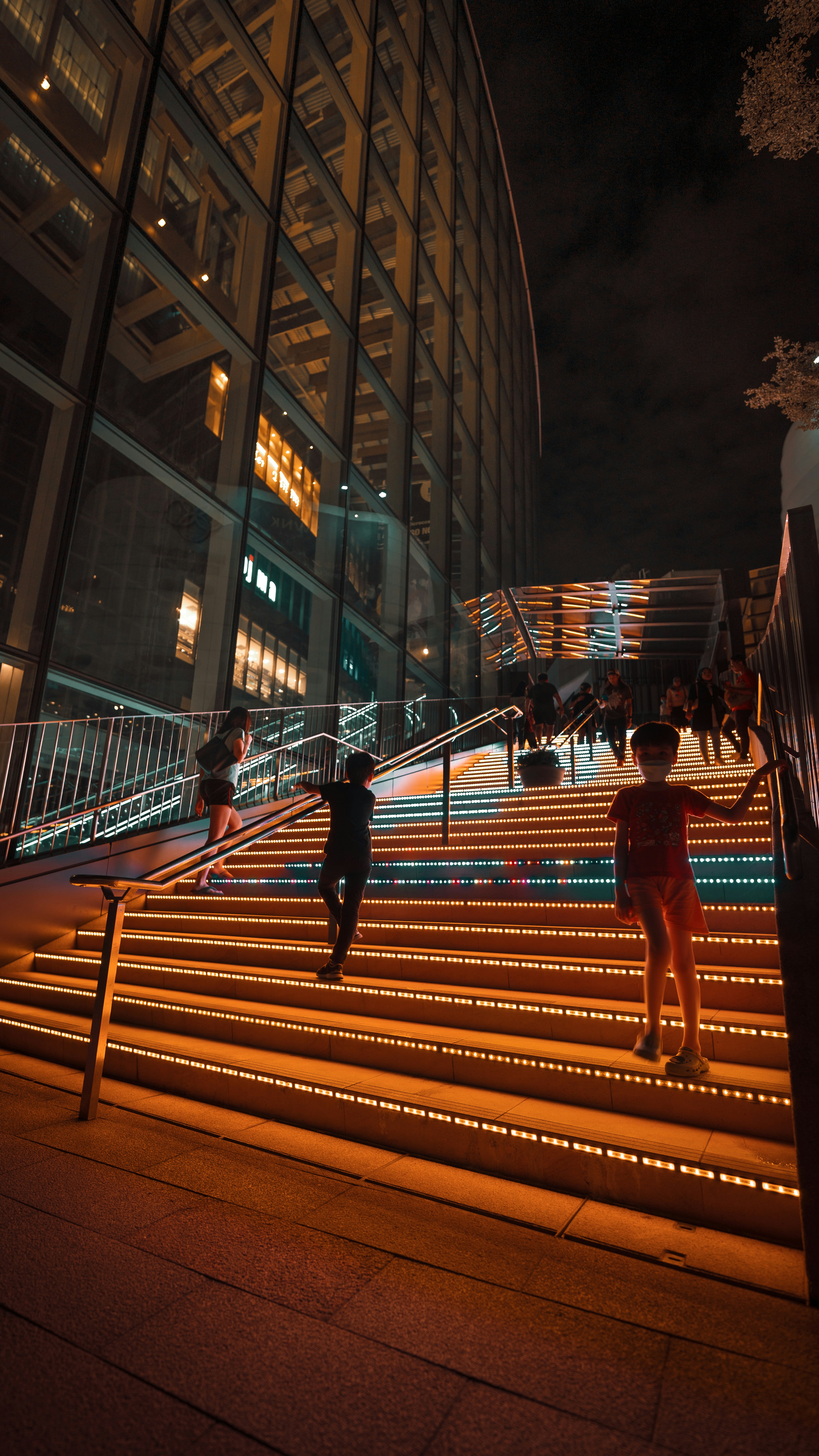 Colorful illuminated stairs leading upward, with children playfully navigating the steps against a backdrop of modern architecture.