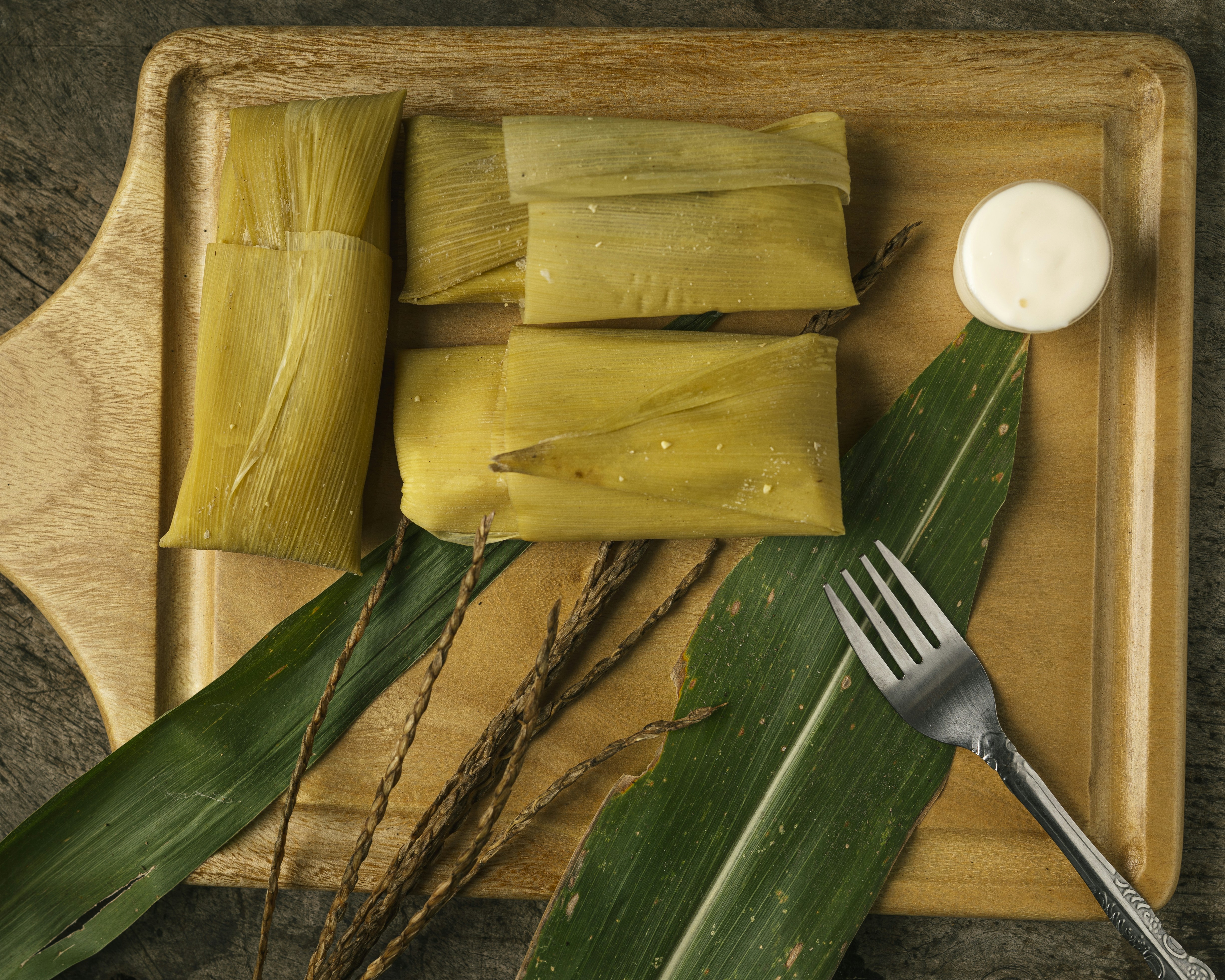 Assorted wrapped foods on a wooden board with a fork and green leaves.
