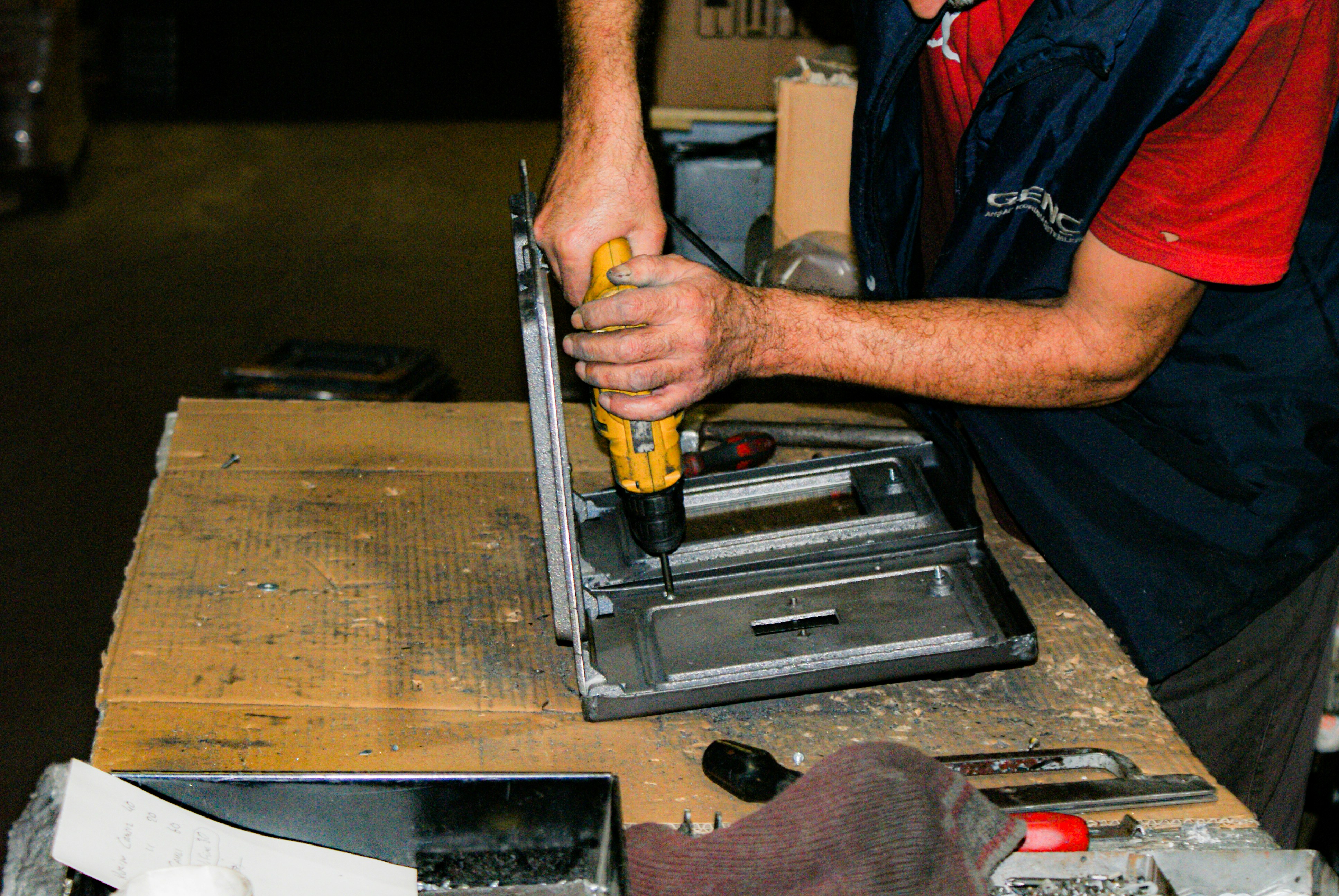 A worker skillfully uses a power drill to assemble a metal frame on a workbench in a workshop environment.