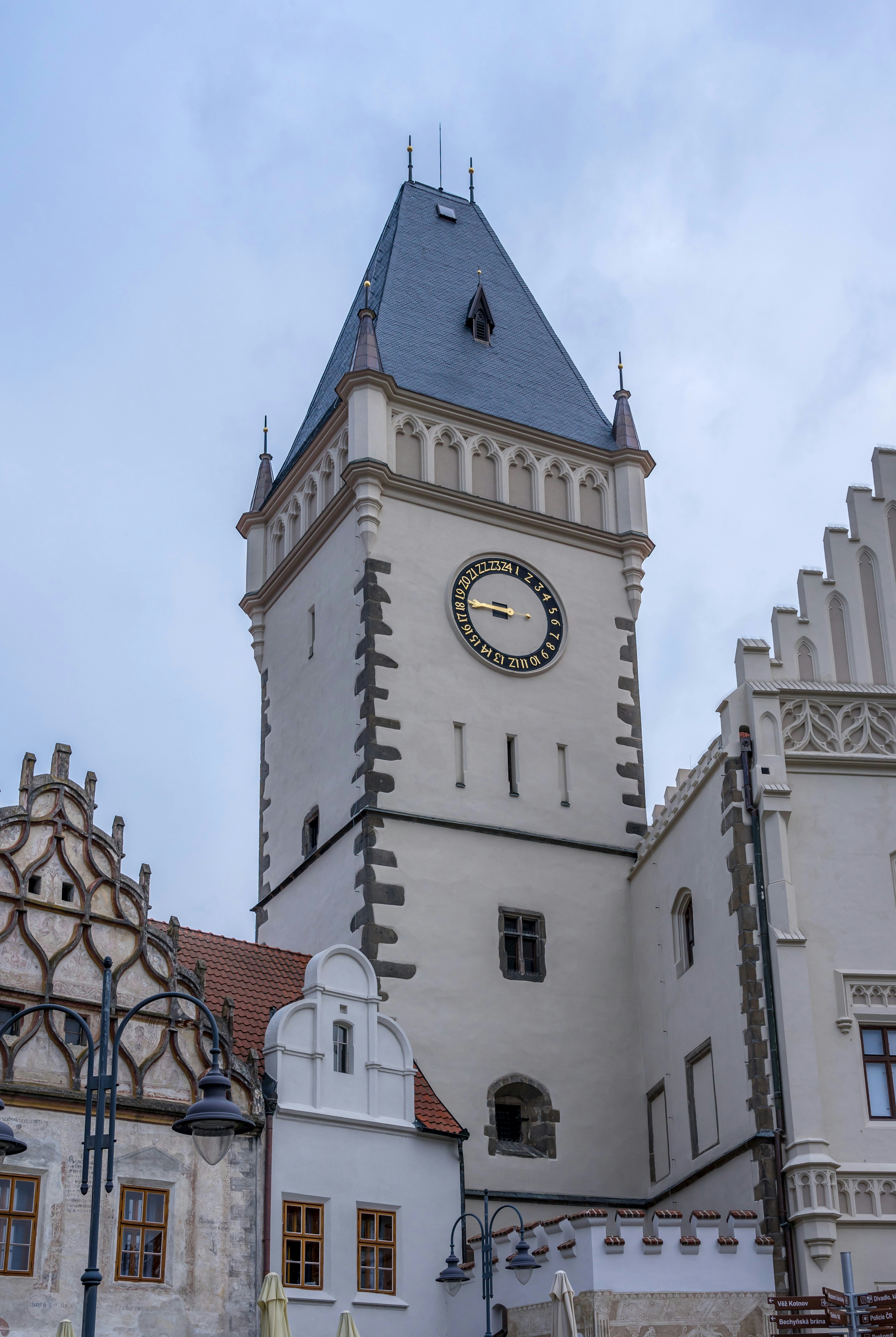 Ornate clock tower with Gothic elements rising above historic buildings under a cloudy sky.