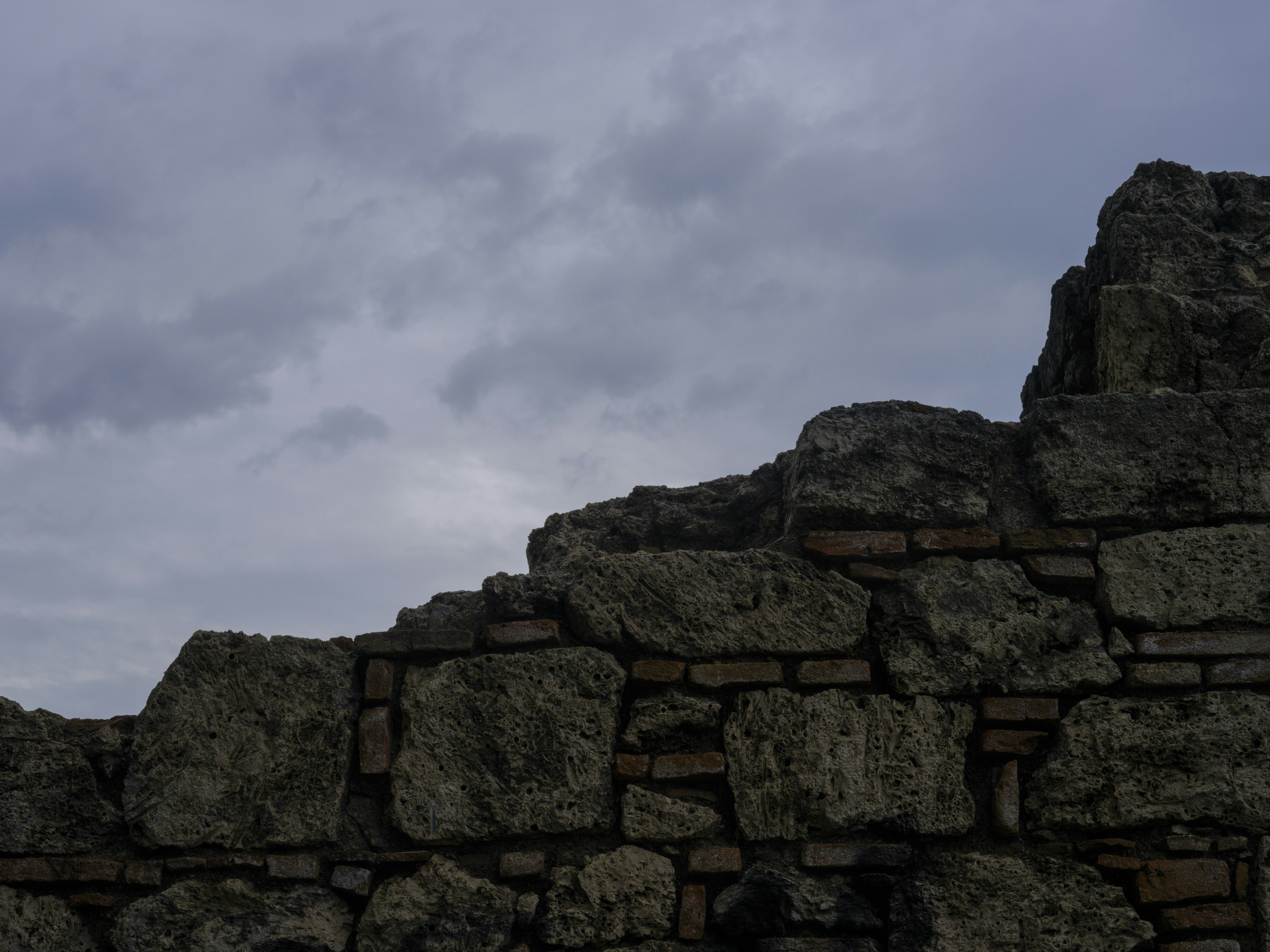 Weathered stone wall against a cloudy sky, showcasing the passage of time and the artistry of ancient builders.