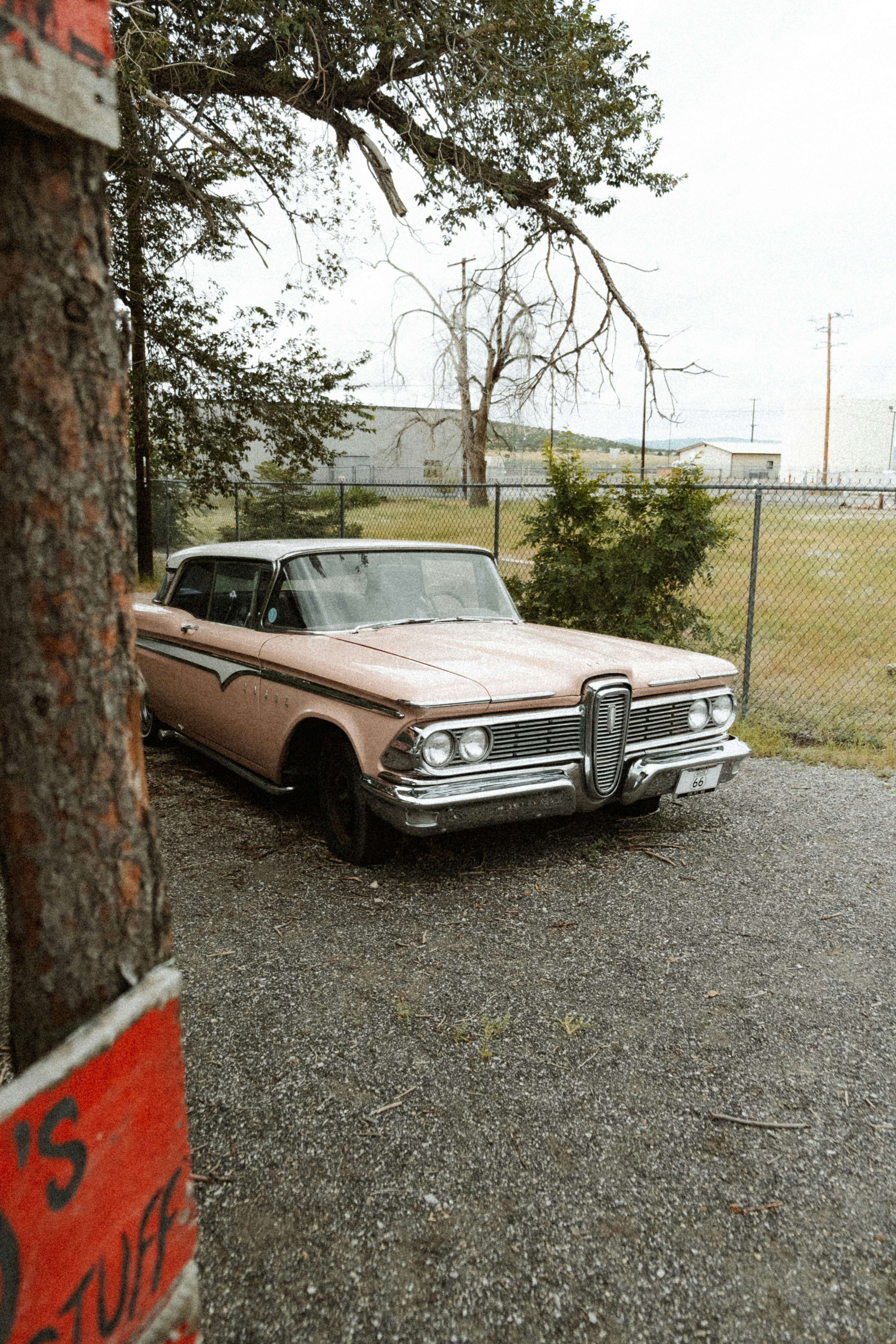 Pastel 1960s Sedan Resting in a Gravel Lot, Framed by a Weathered Fence