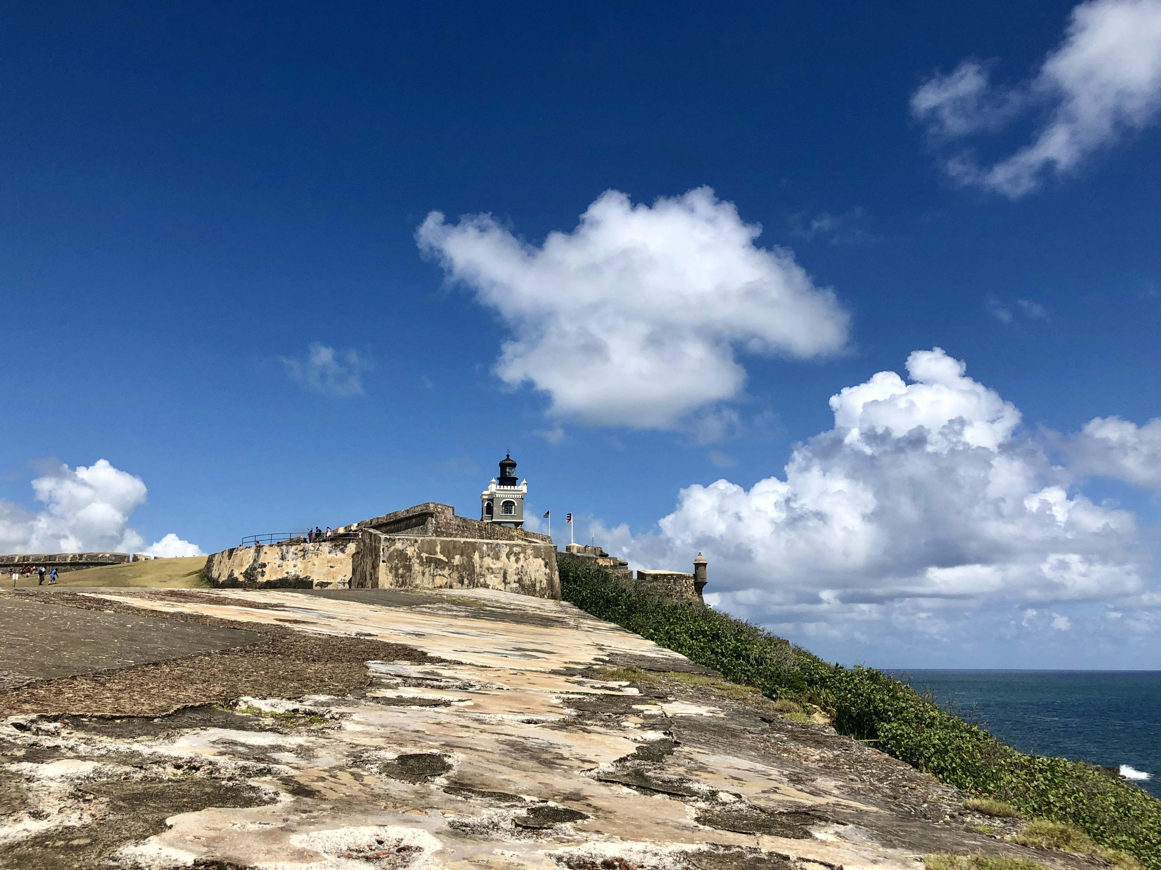 Historic fort perched atop a coastal hill under a vibrant blue sky with scattered clouds.