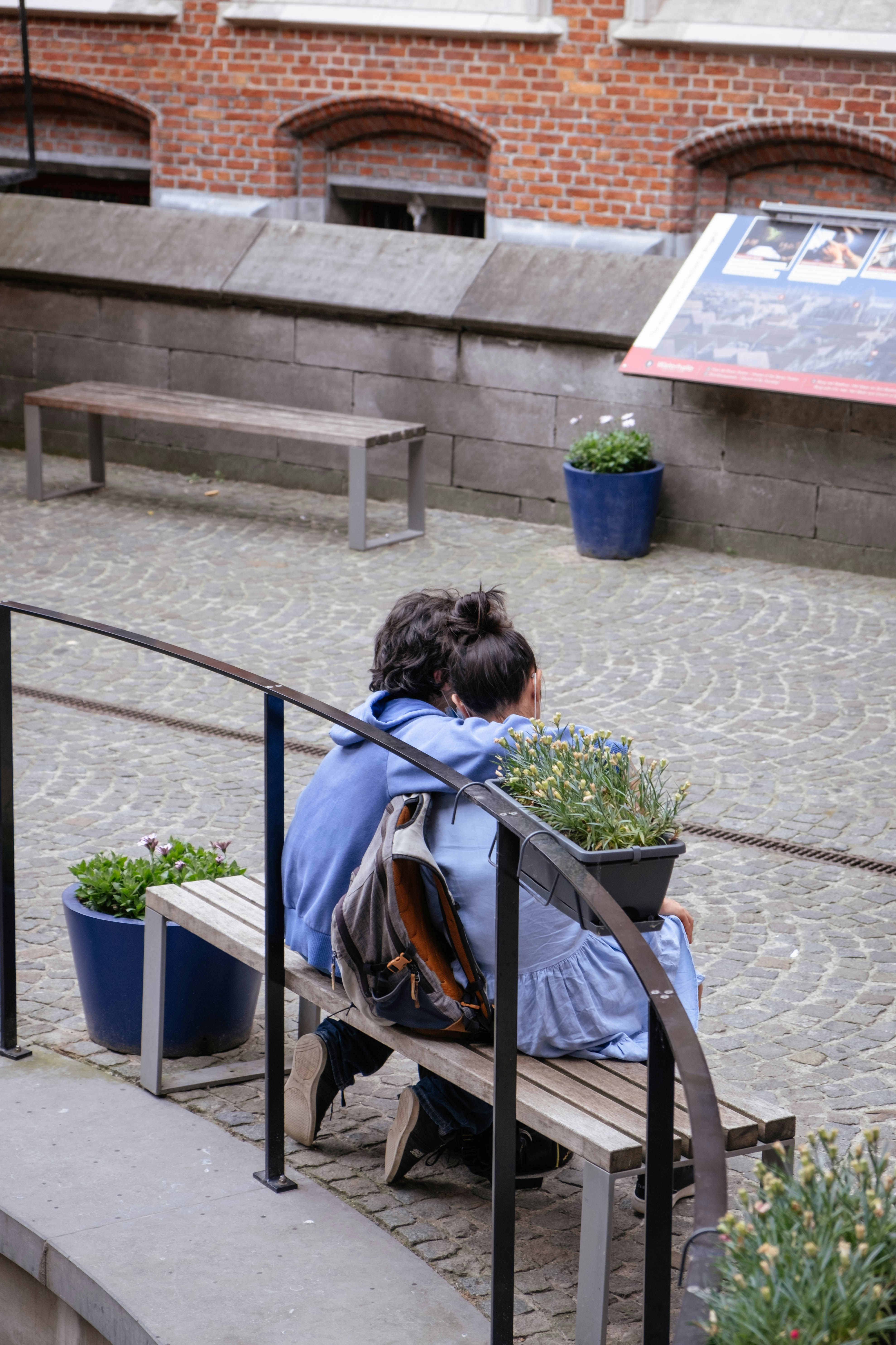Couple on a bench, urban courtyard with potted plants and a leaning display