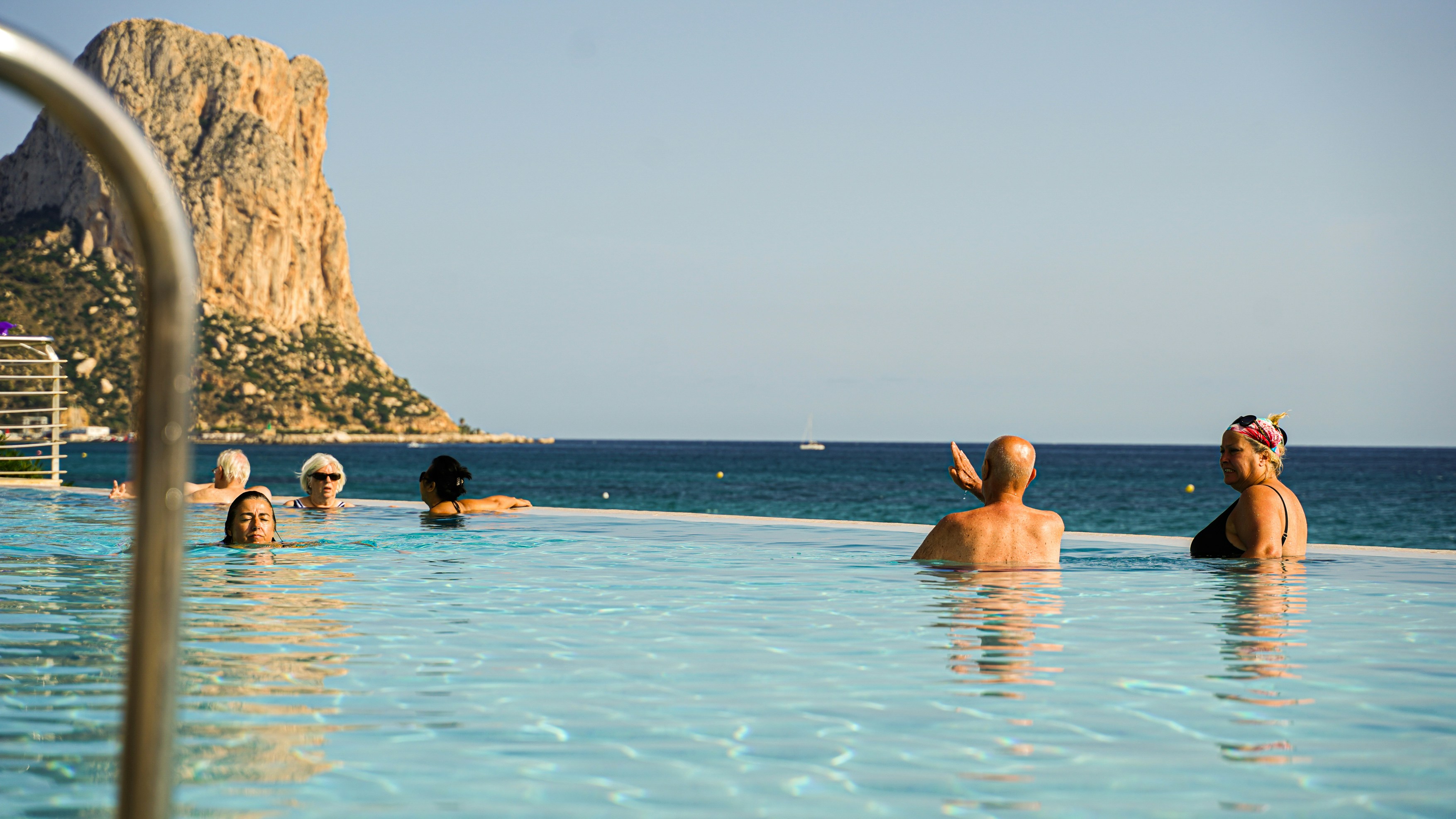 Cliffside Poolside: Sunlit Bathers Framed by a Calm Azure Sea