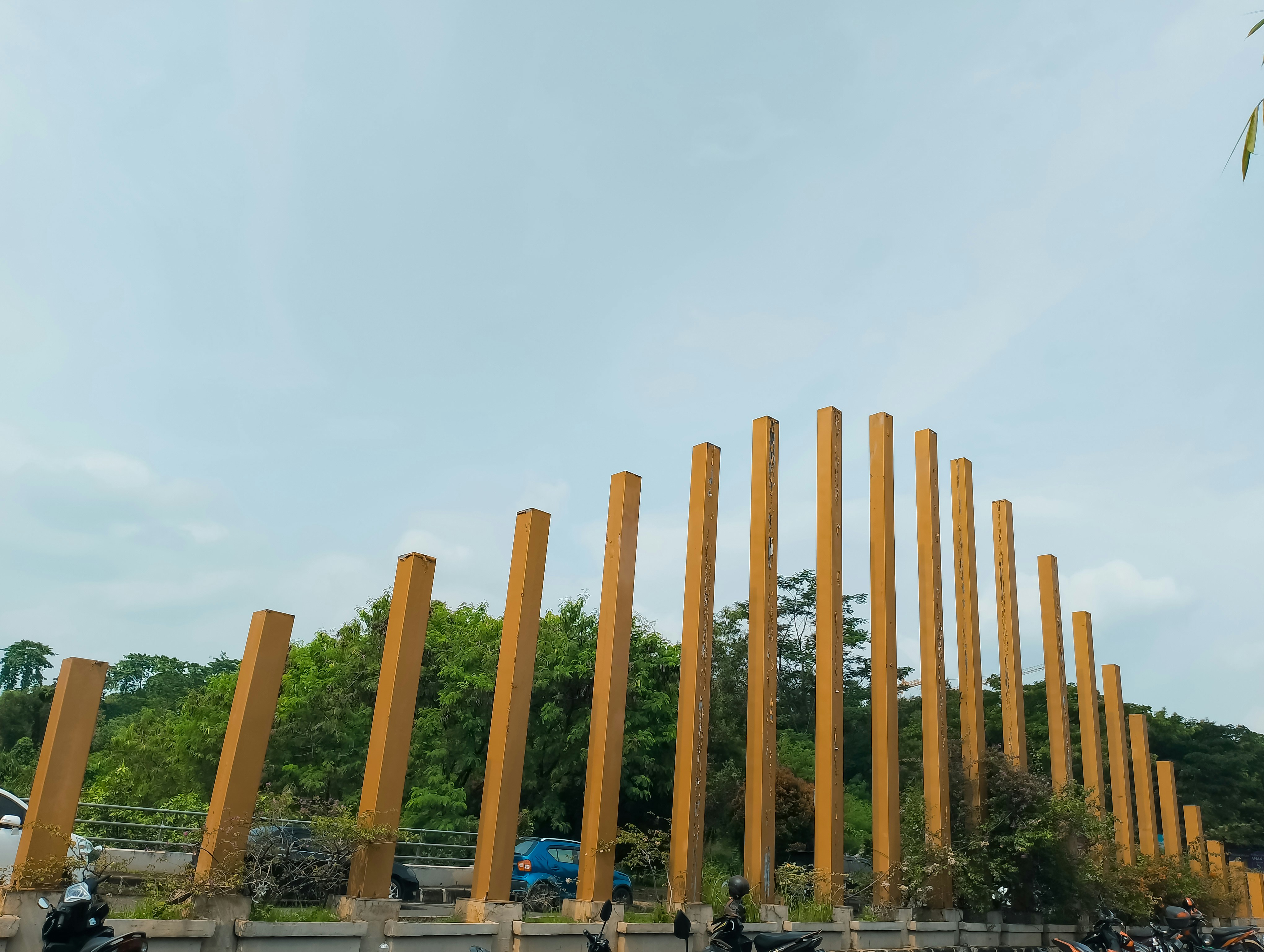 A striking arrangement of tall yellow poles against a backdrop of lush greenery, showcasing modern architectural design.