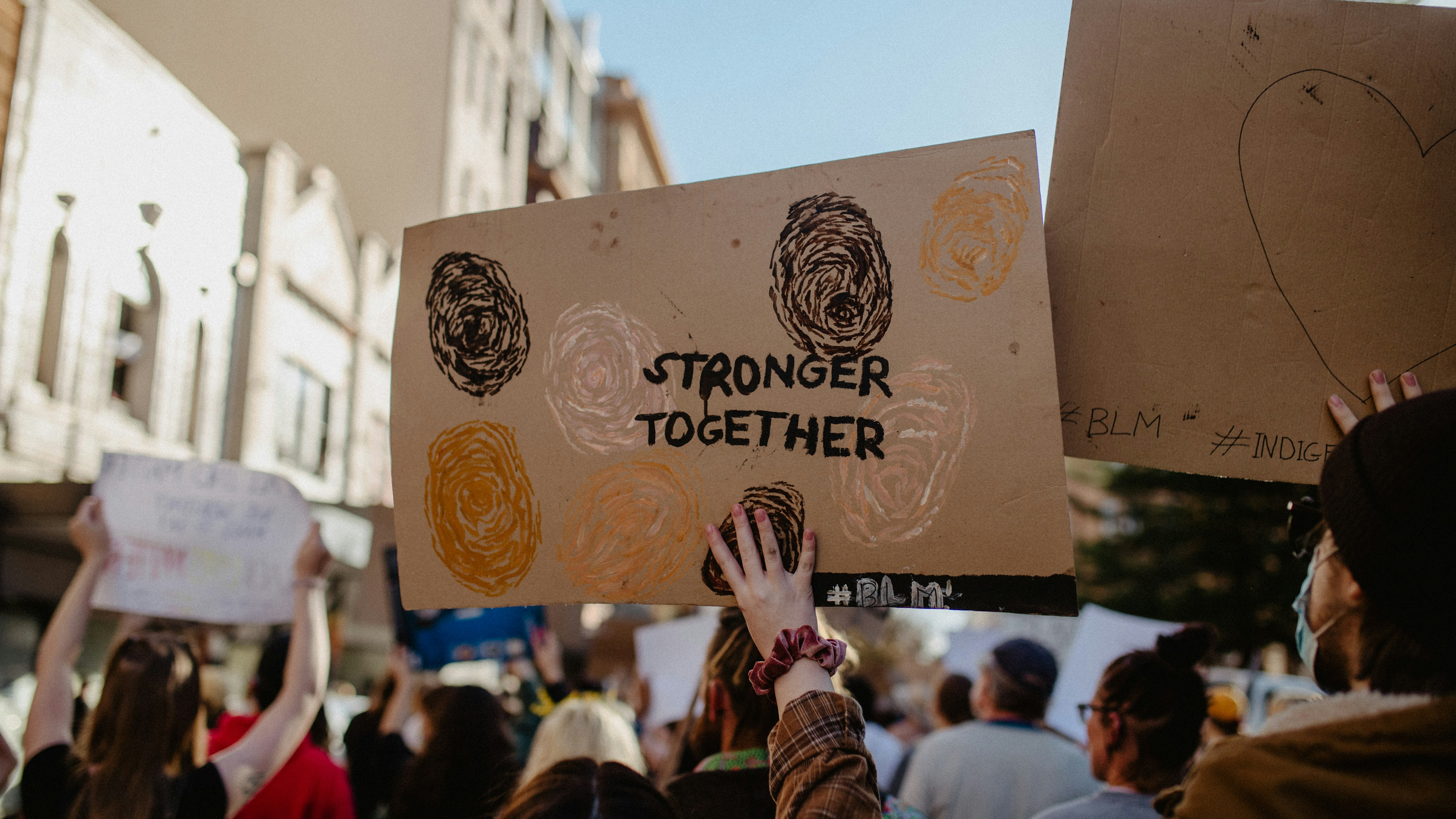 Protesters holding signs advocating for unity and social justice during a vibrant demonstration. The focus is on a sign that reads 'Stronger Together.'