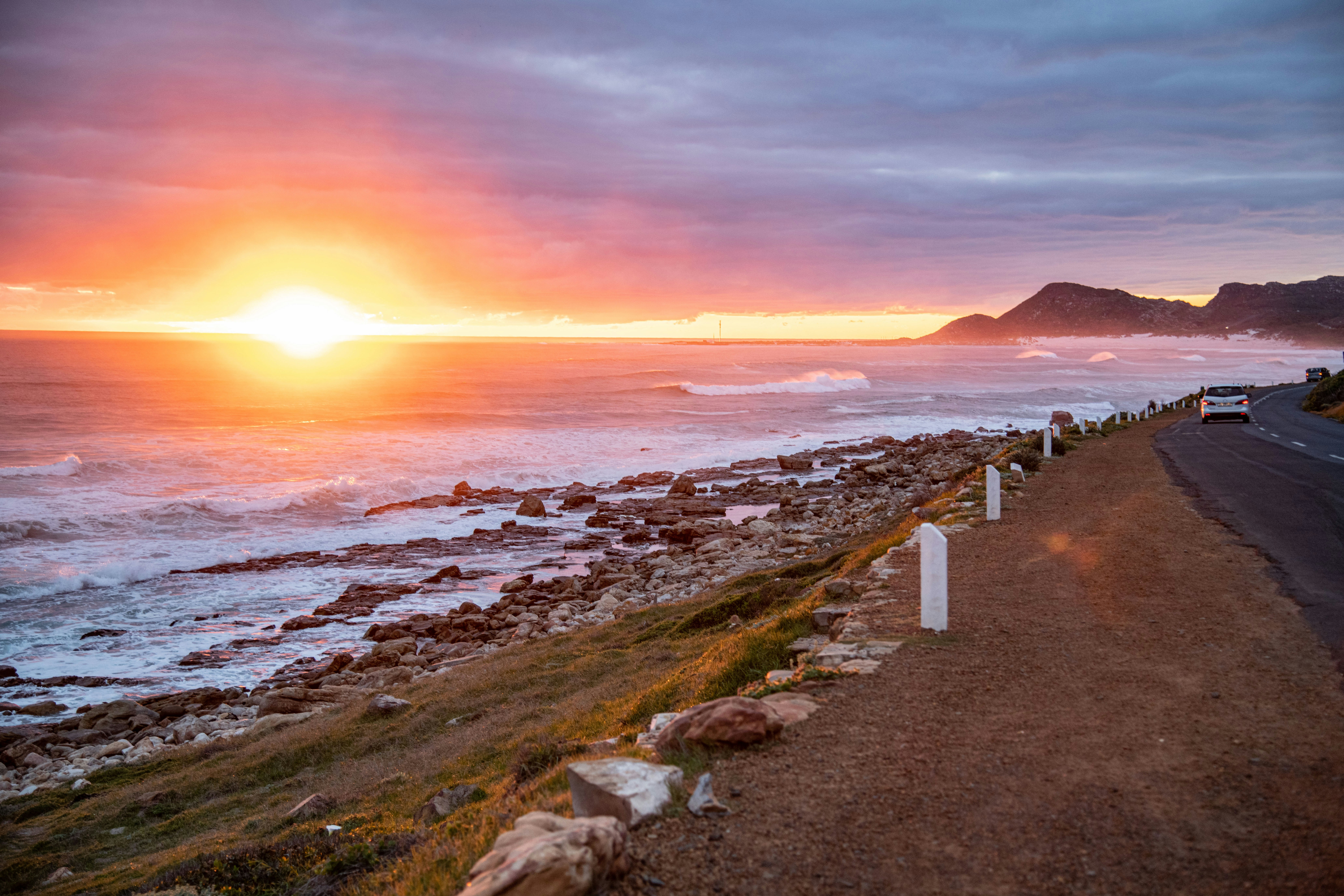 Sunflare over rugged coastline road at sundown