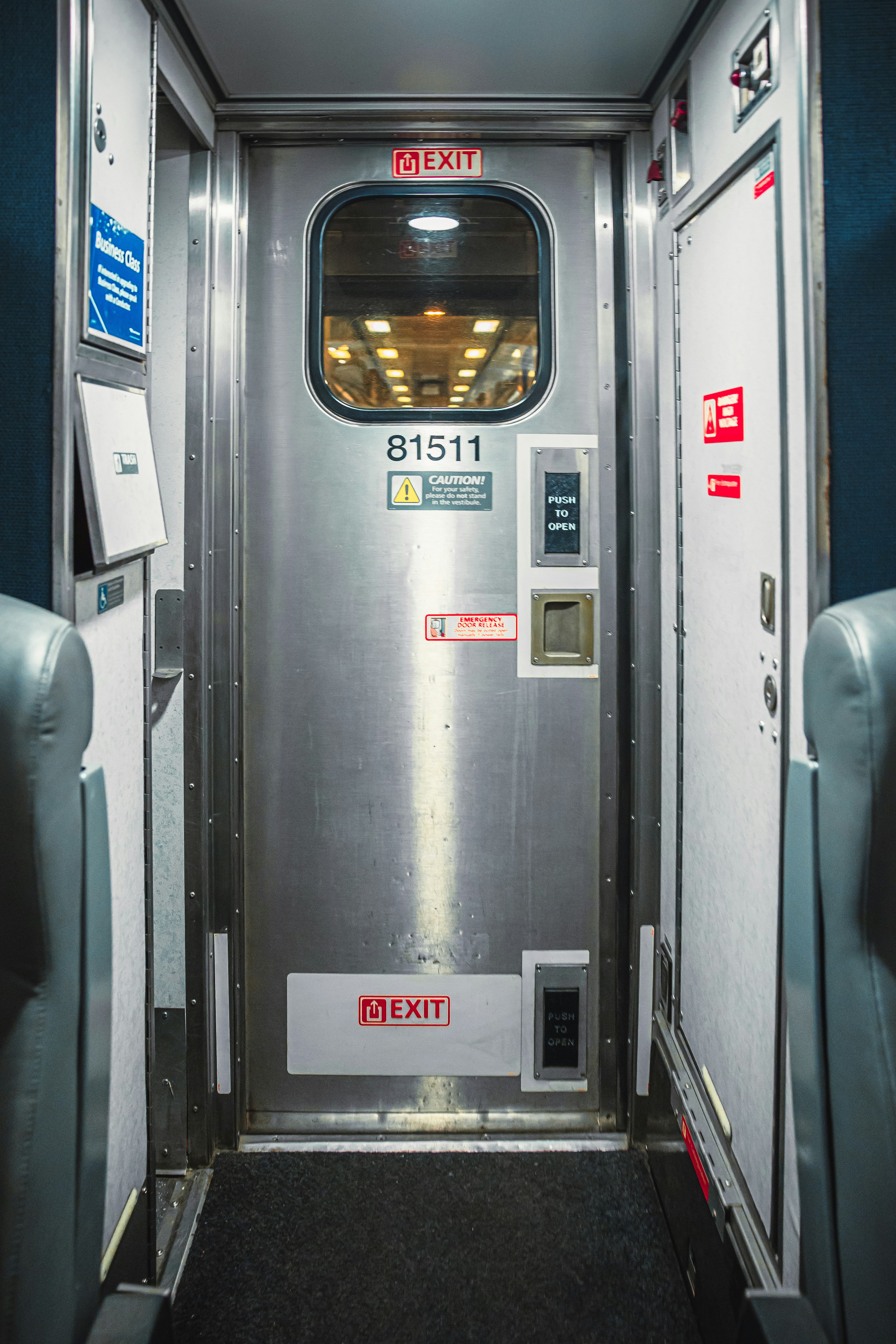Metal exit door of a train compartment, featuring safety signs and a visible window. The interior showcases a blend of functionality and design.