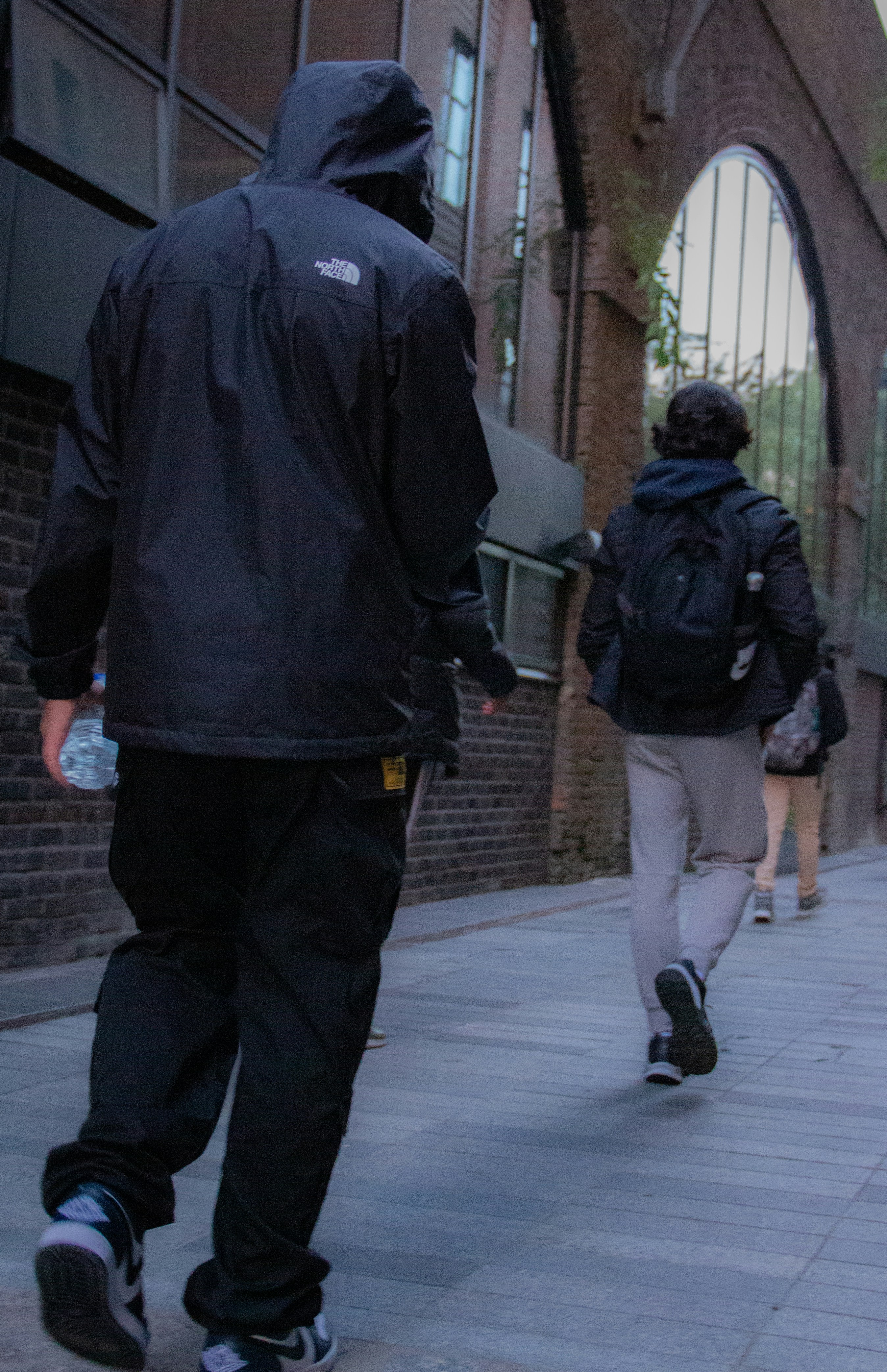 Shadowed Footpath: Hooded Figures in a Brick Alley