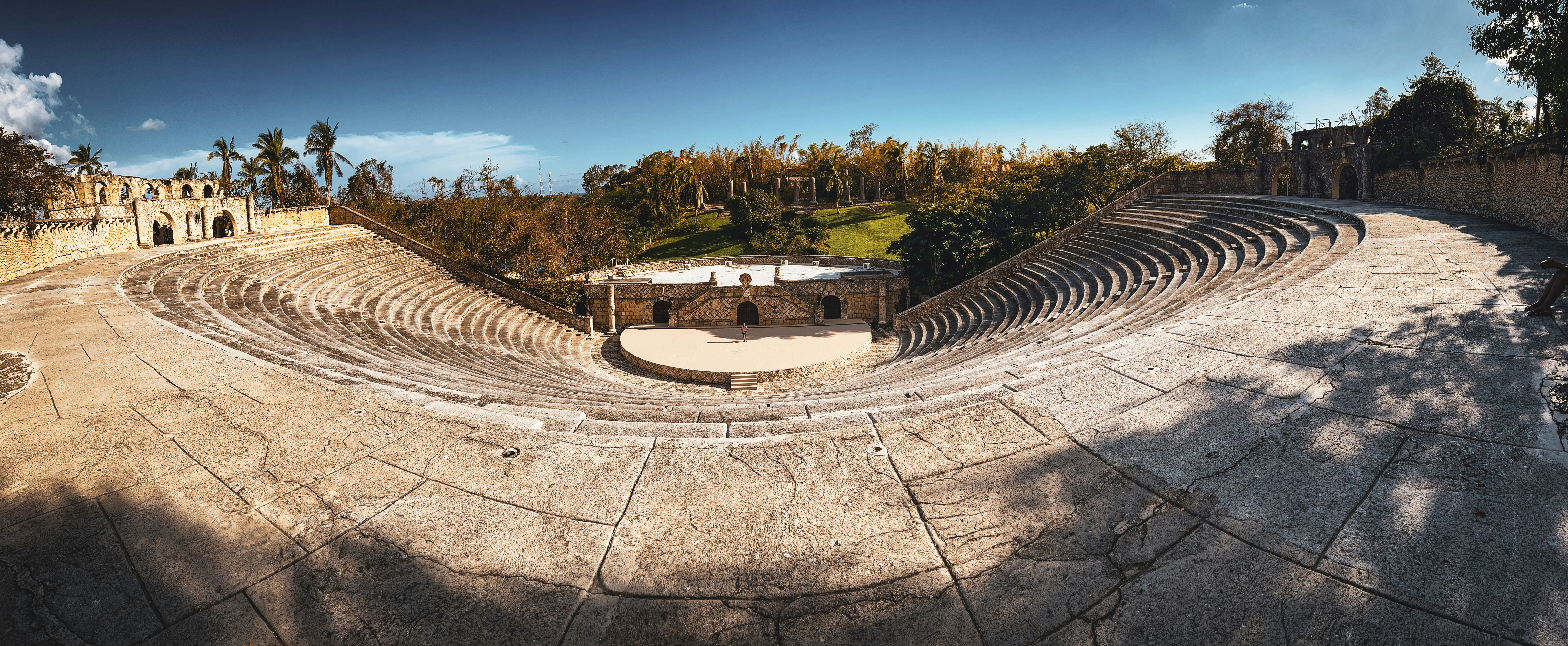 Panoramic view of an ancient amphitheater surrounded by lush greenery, showcasing its architectural grandeur and historical significance.