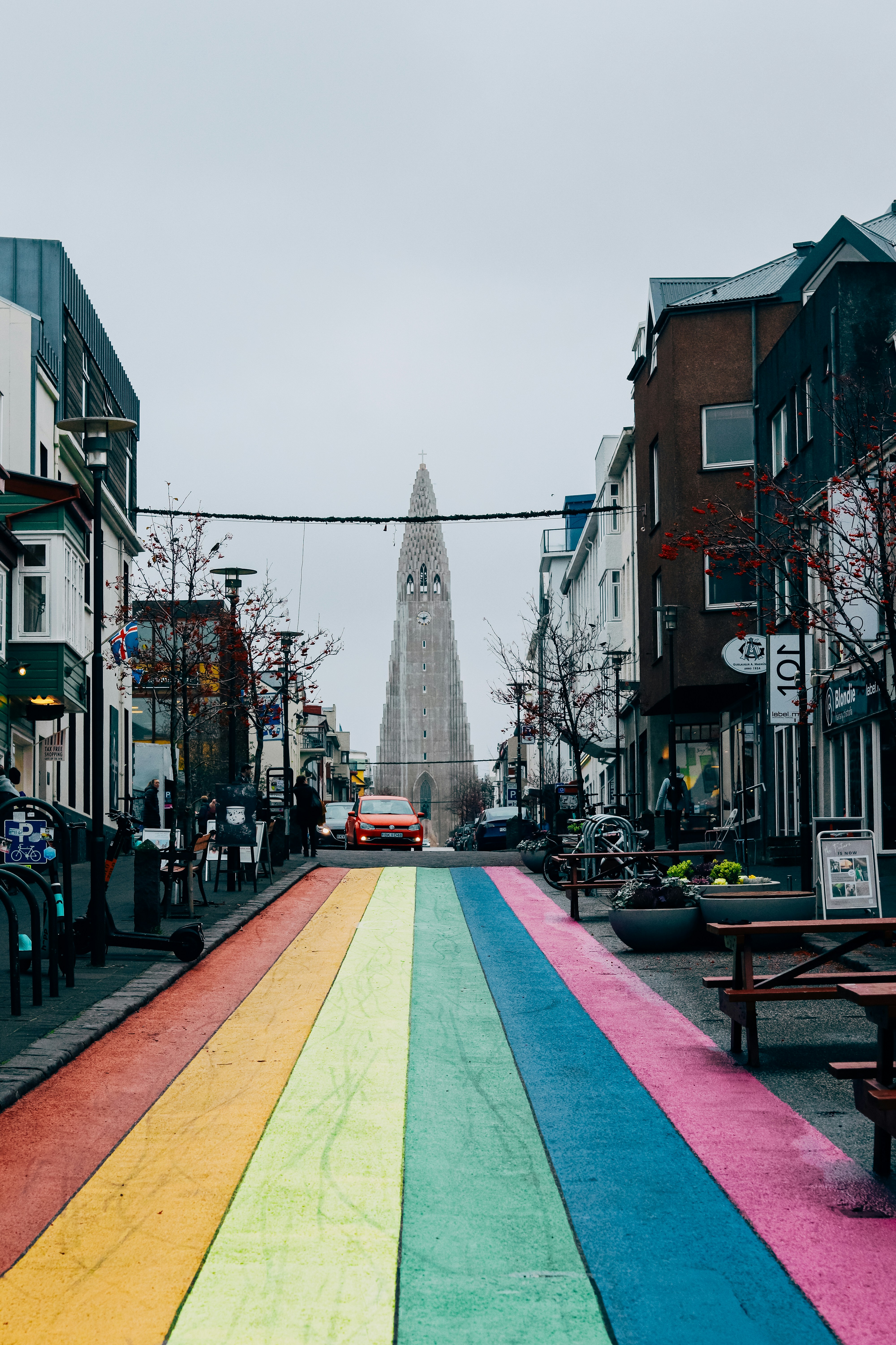 Colorful rainbow street leads the eye towards a striking church spire in a lively urban setting. The scene captures the essence of community and artistic expression.