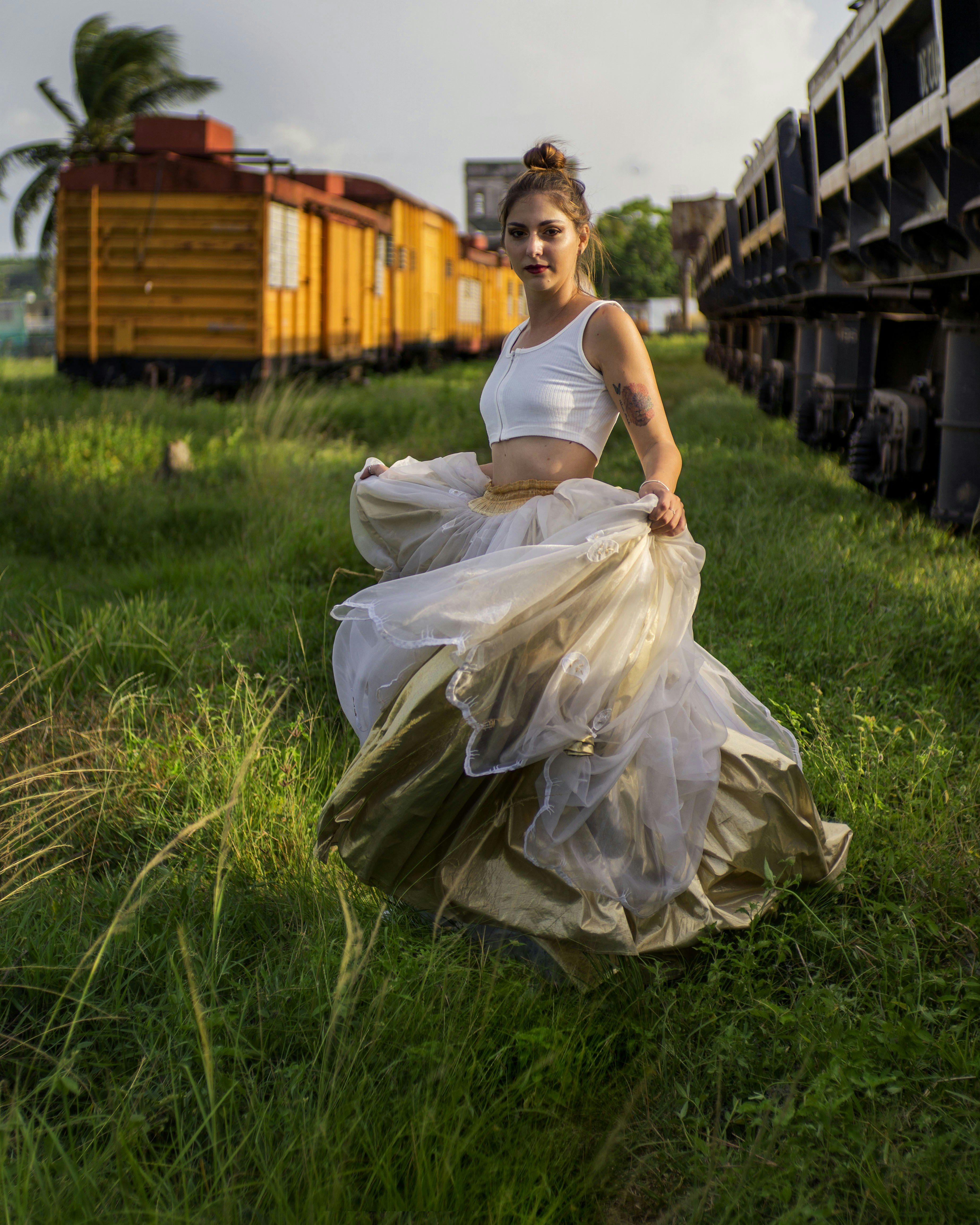 A woman twirls gracefully in a flowing skirt, surrounded by lush grass and vintage train cars, capturing a moment of joy and movement.