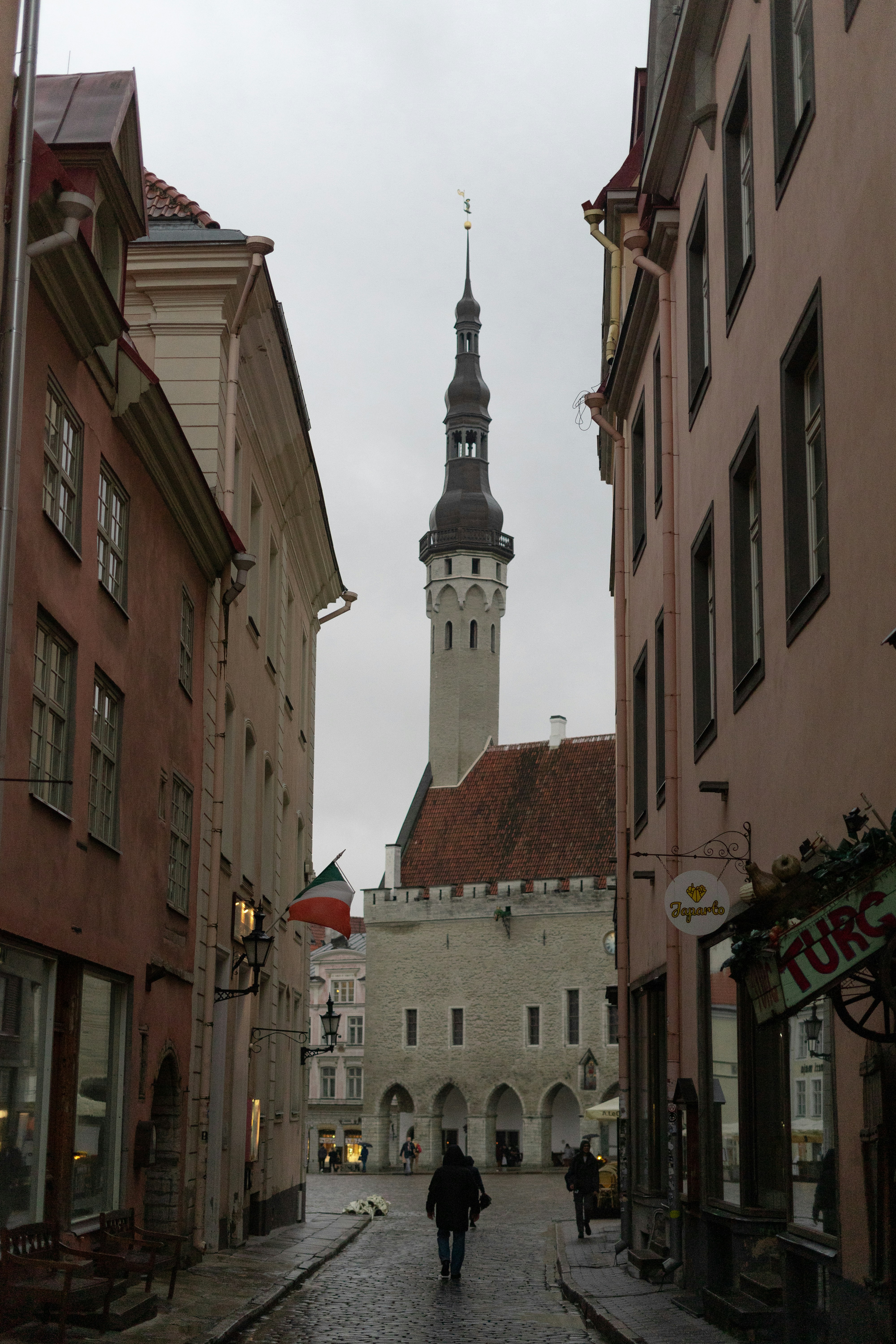 Narrow cobblestone street framed by pastel buildings leading to a prominent clock tower, embodying Tallinn's medieval architecture.
