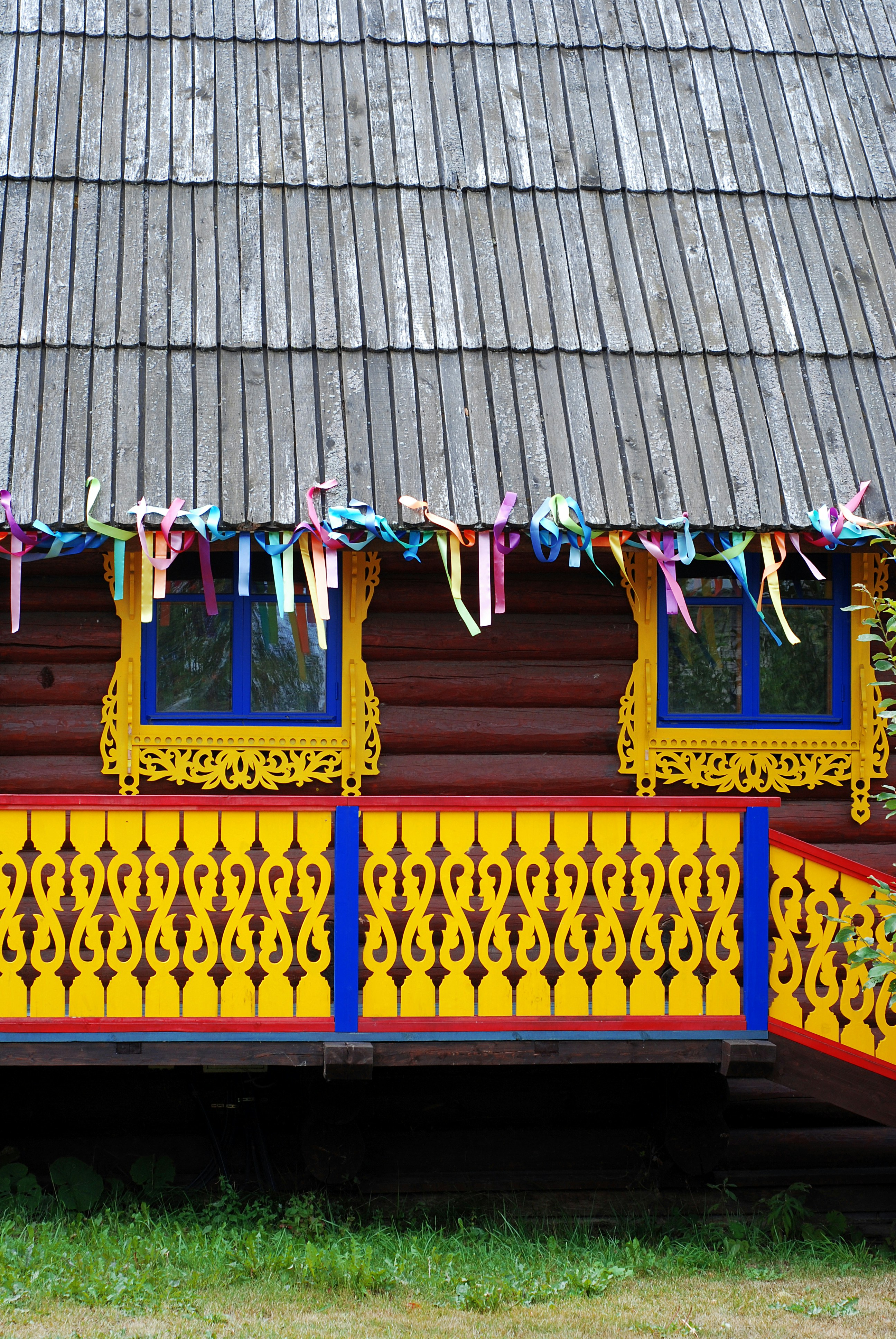 Vibrantly painted wooden house featuring intricate yellow and blue details, with colorful ribbons embellishing the roofline.