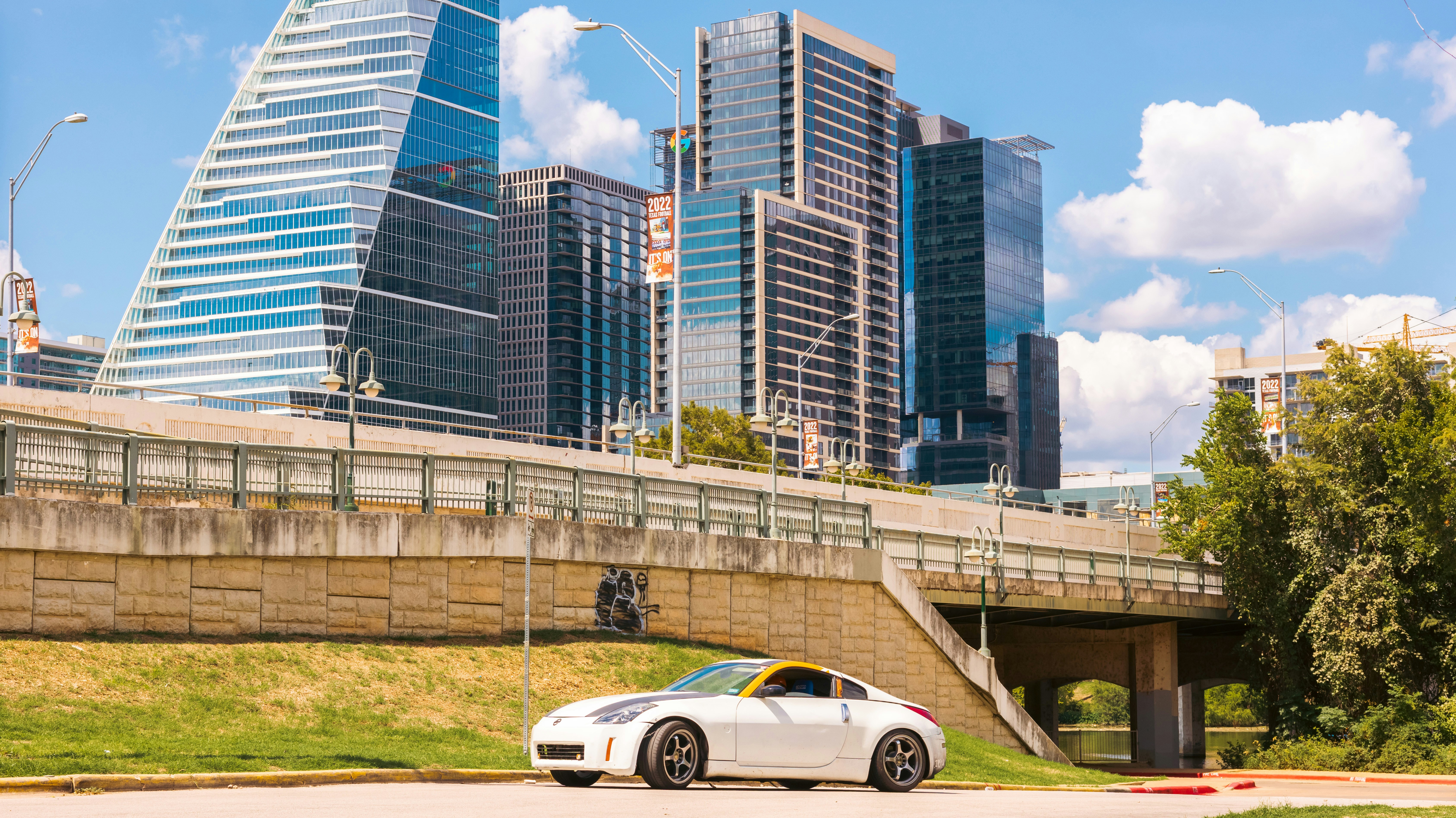 White sport coupe anchors the riverfront beneath a sculpted glass skyline.