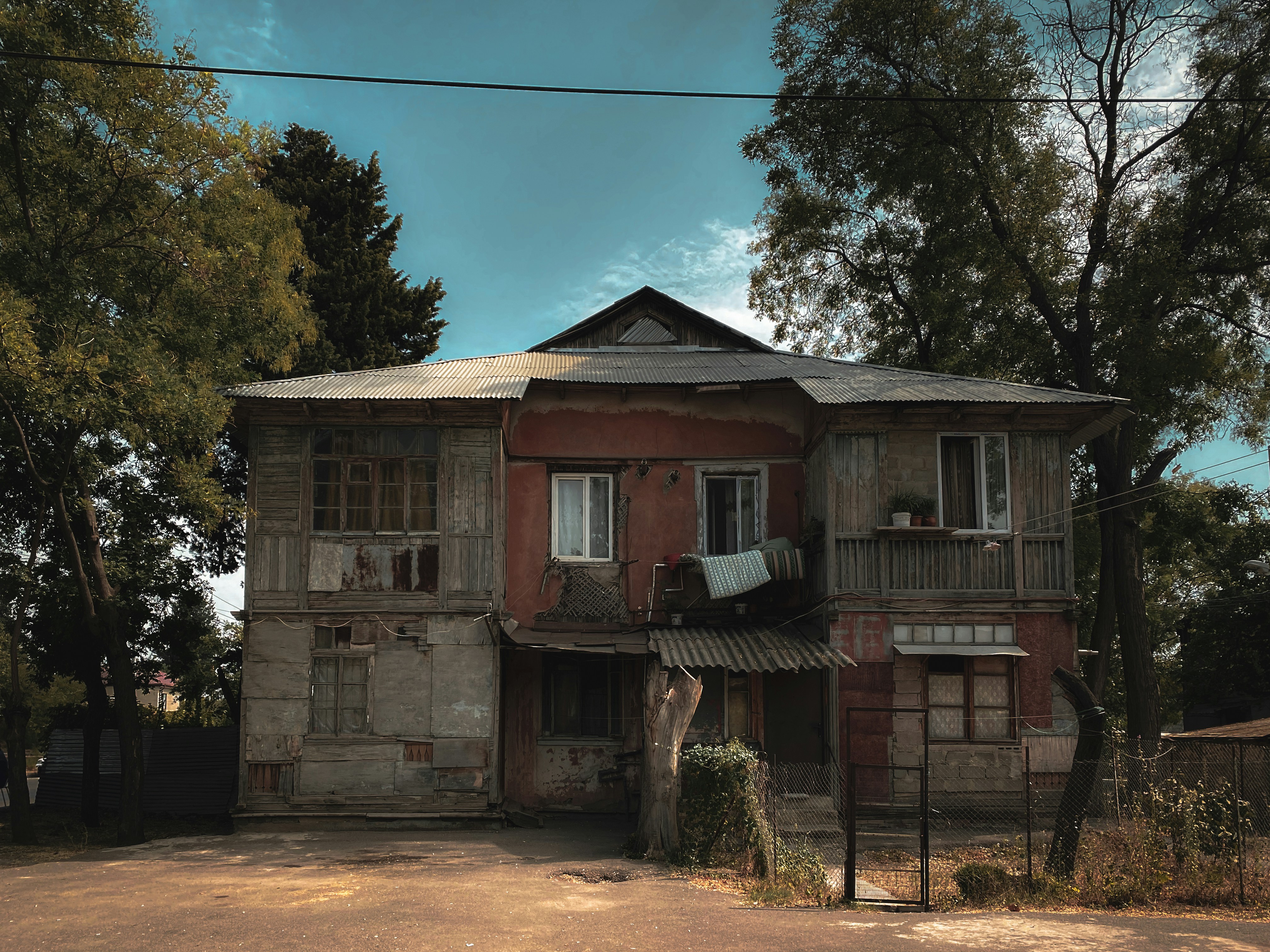 Dilapidated two-story house with peeling paint and overgrown vegetation, reflecting a sense of history and neglect.
