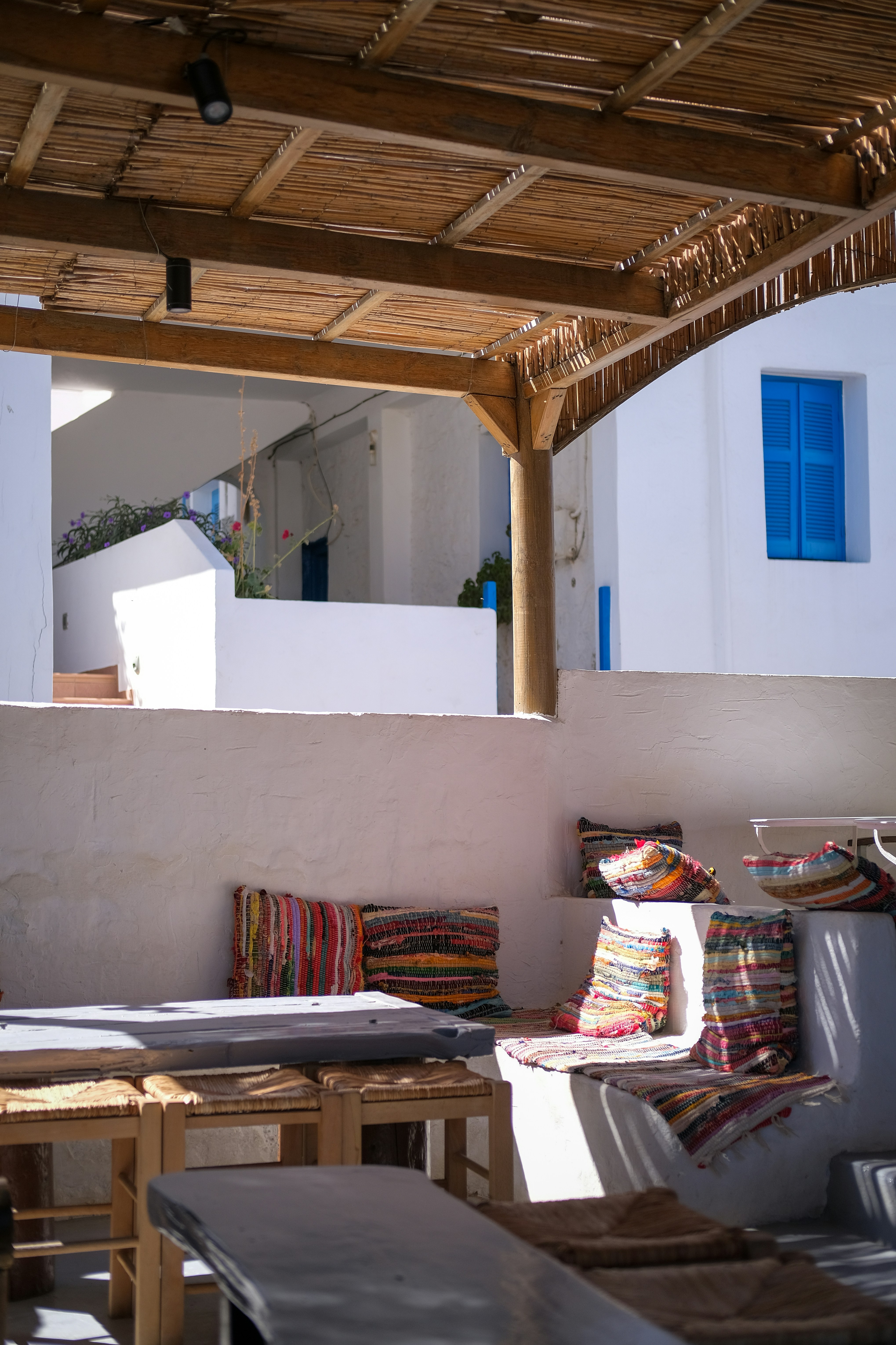 Sunlit Cycladic Terrace: Blue Window Framed by White Walls and a Woven Roof