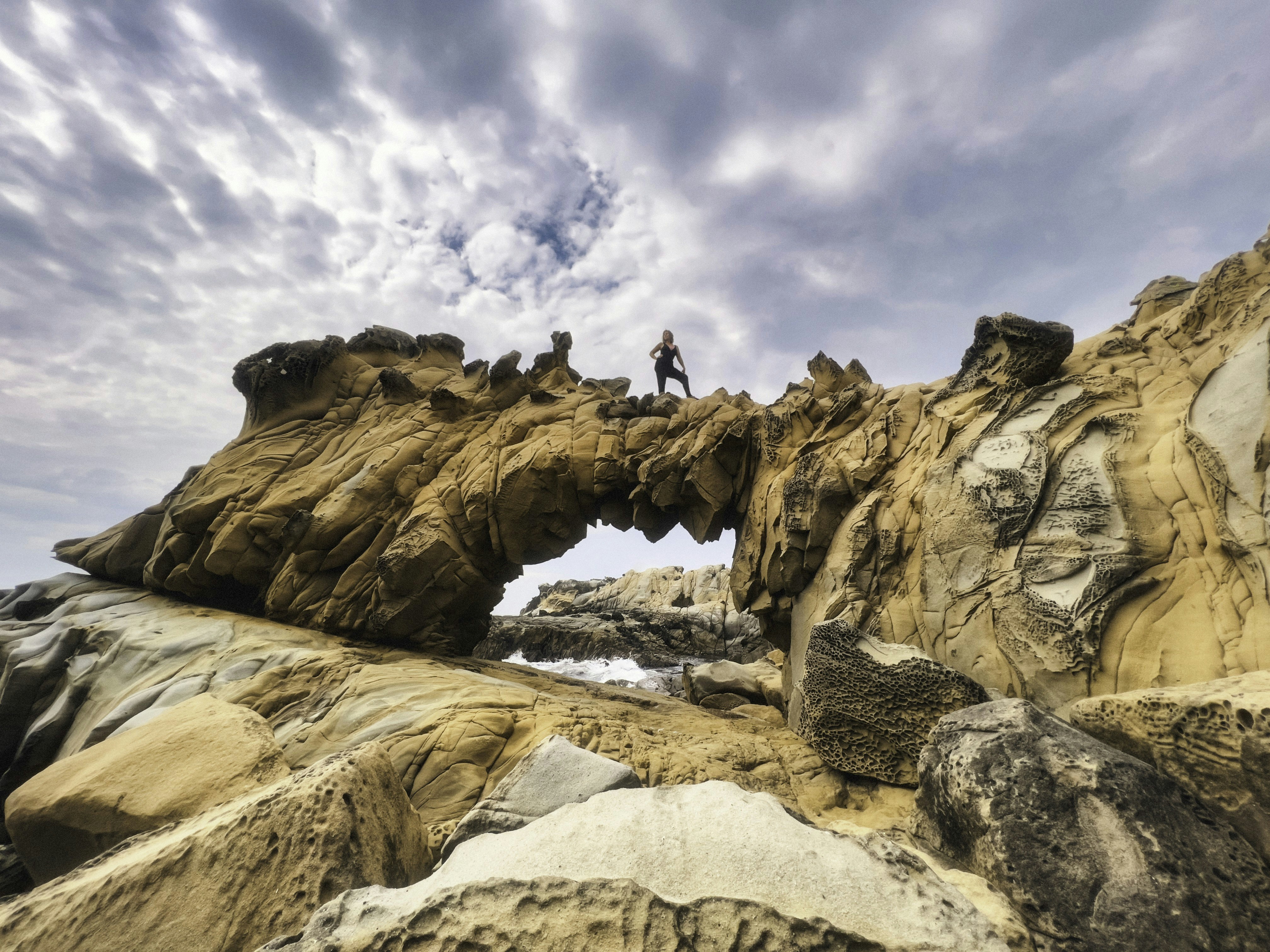  Lone figure atop a natural stone arch balancing against a dramatic seascape