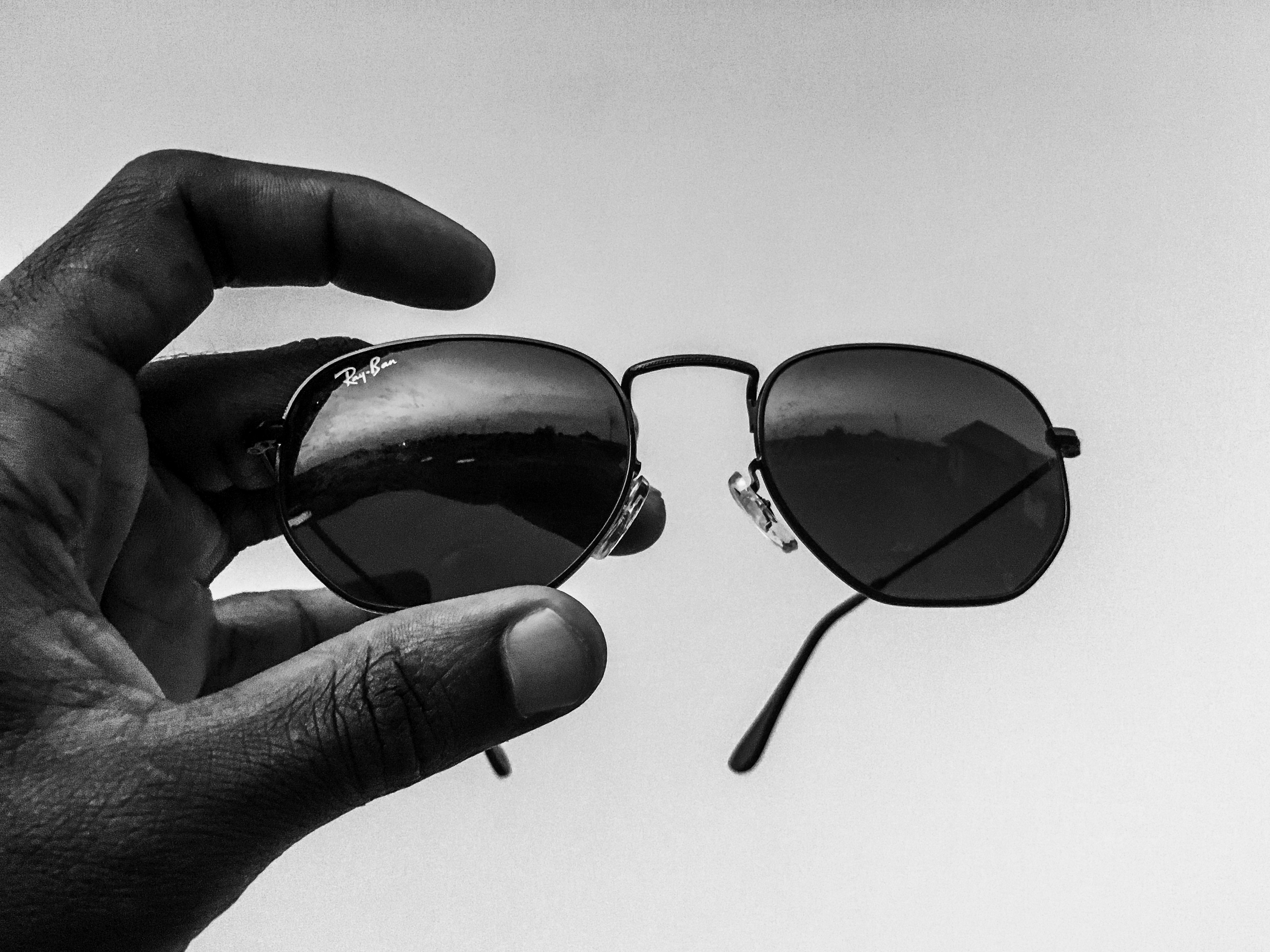 Hand holding sleek sunglasses against a plain backdrop.