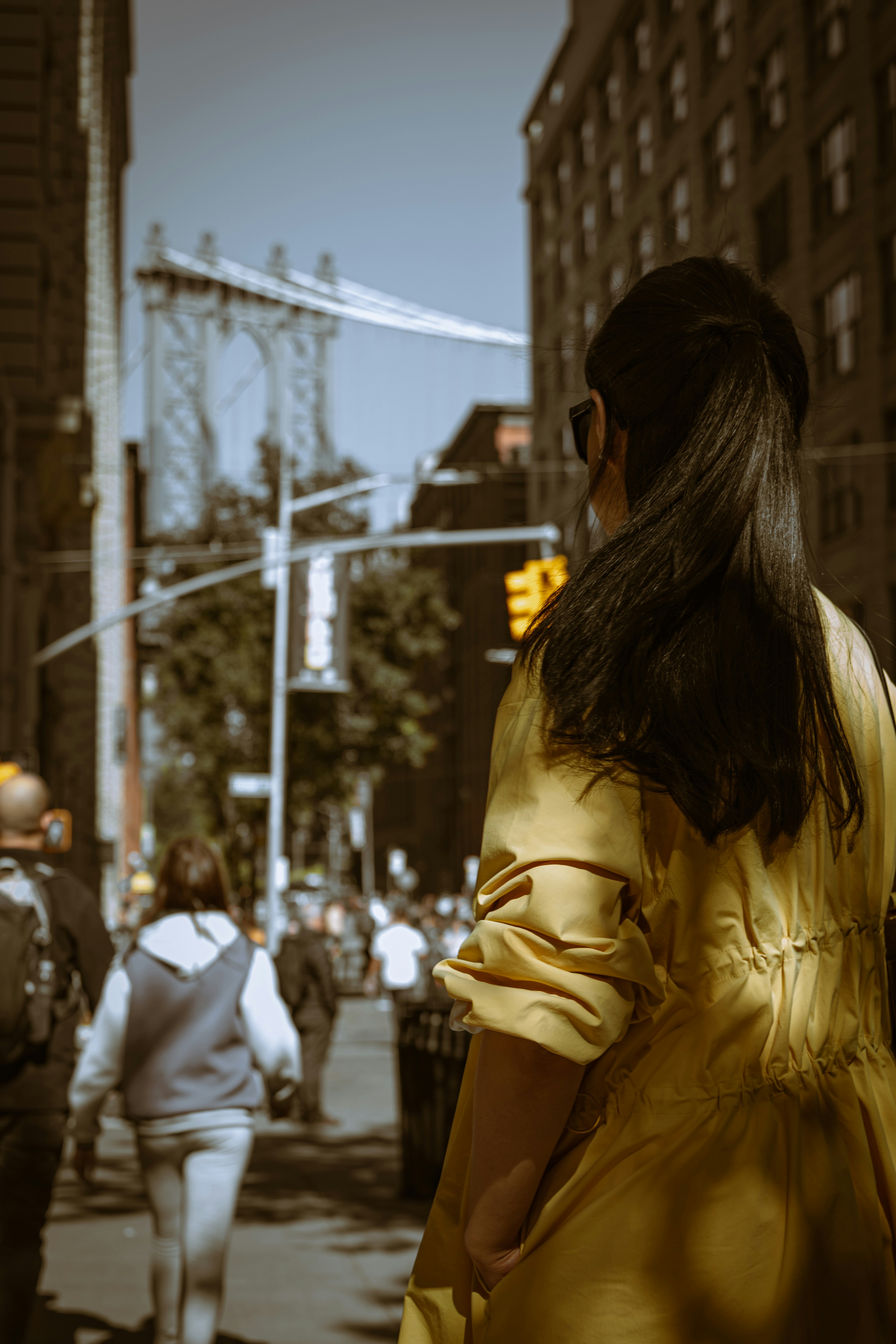 Woman in a yellow coat gazes toward the bridge and city street