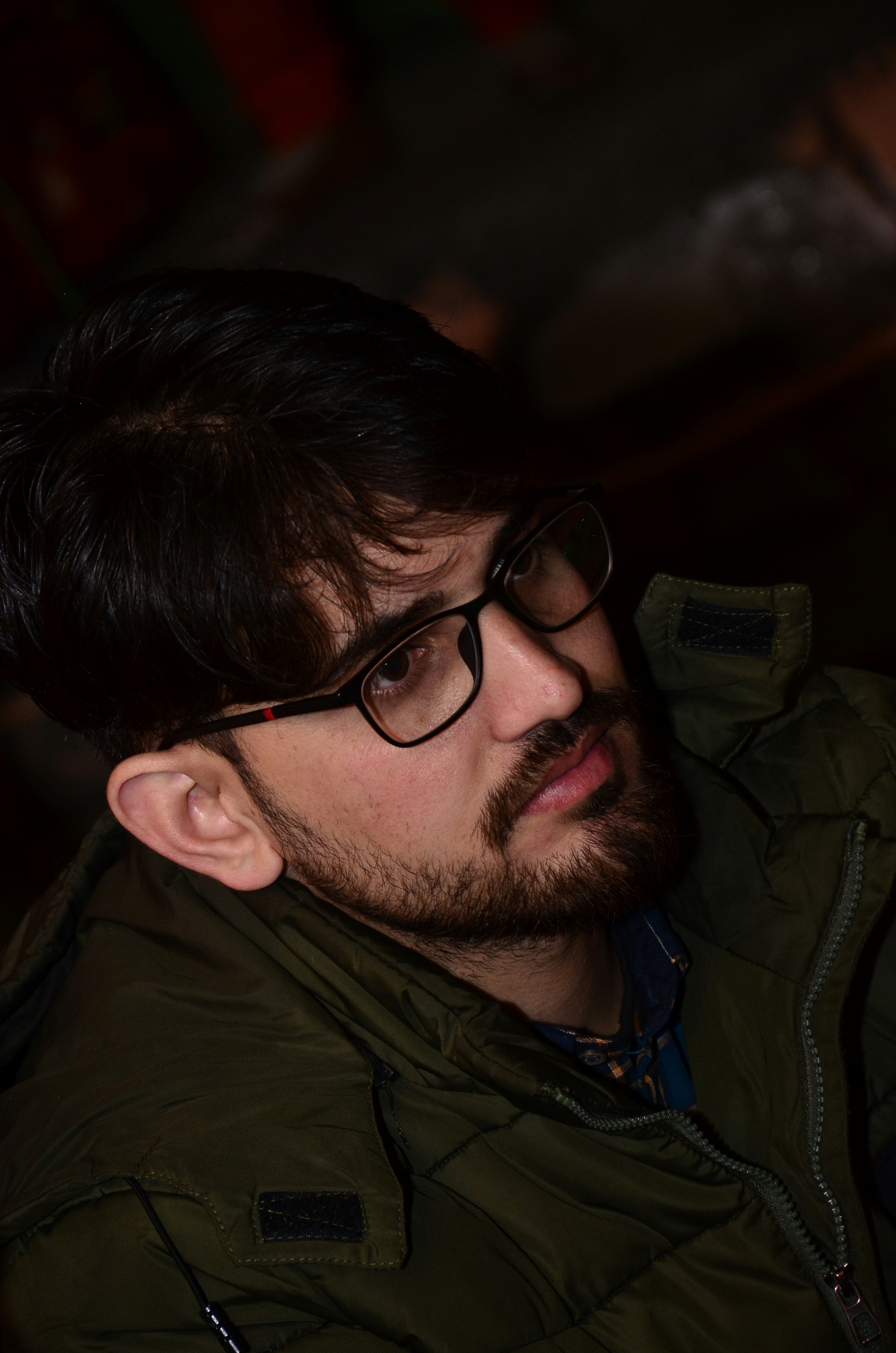 Man with glasses in a dark green jacket gazes thoughtfully to the side.