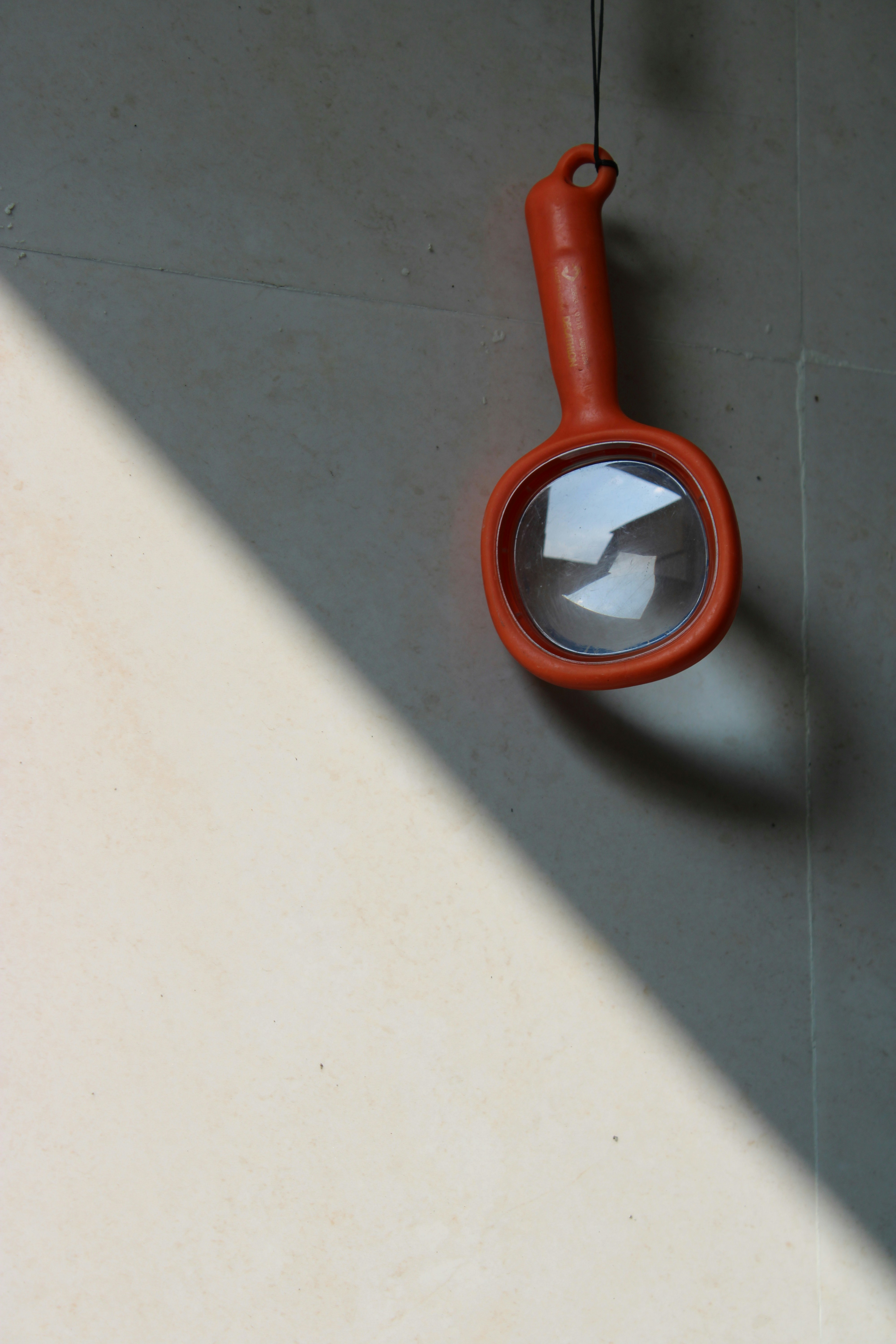 Orange magnifying glass hanging against a light-colored wall, casting a shadow that creates a striking contrast.