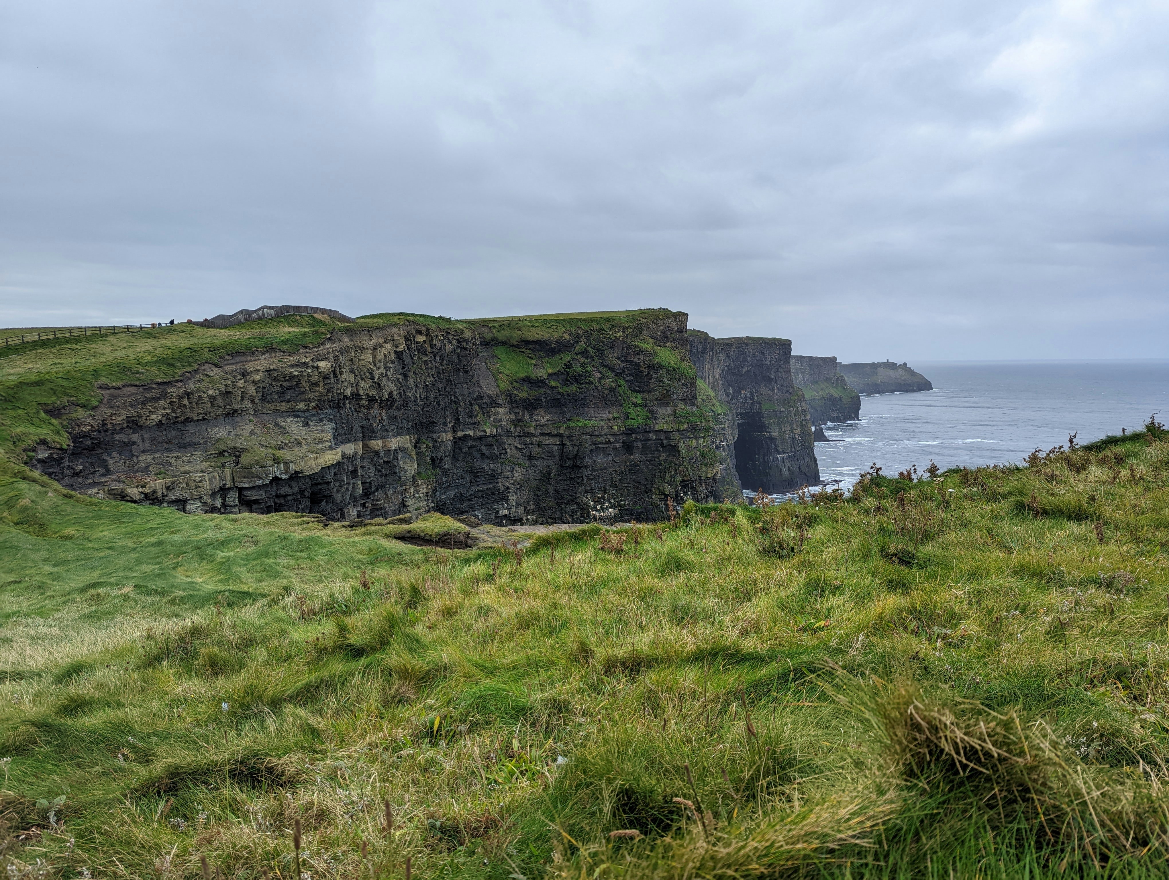 Grass-topped cliffs overlooking the Atlantic Ocean under a cloudy sky.
