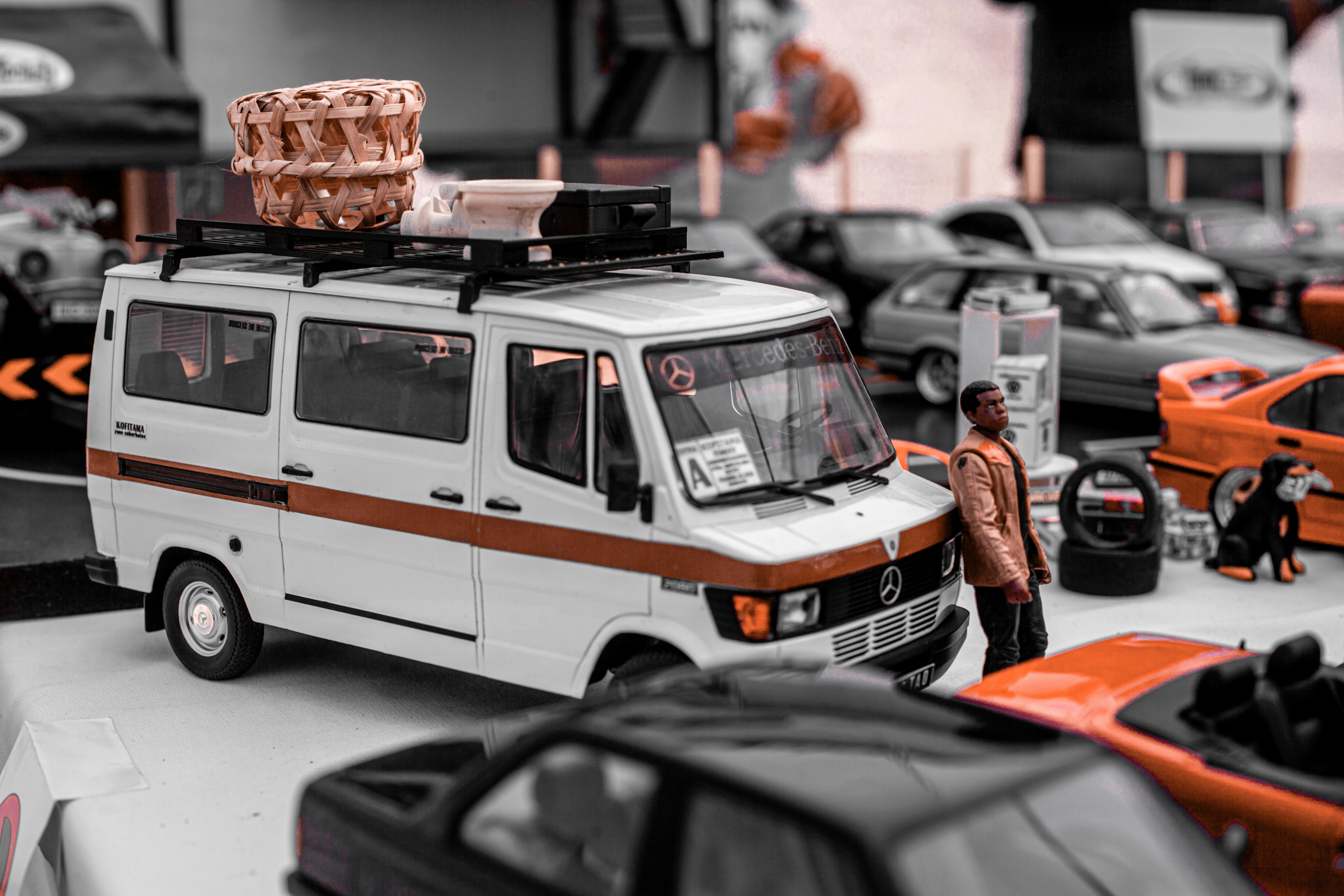 White Mercedes van with orange stripe and rooftop cargo anchors a car-show display