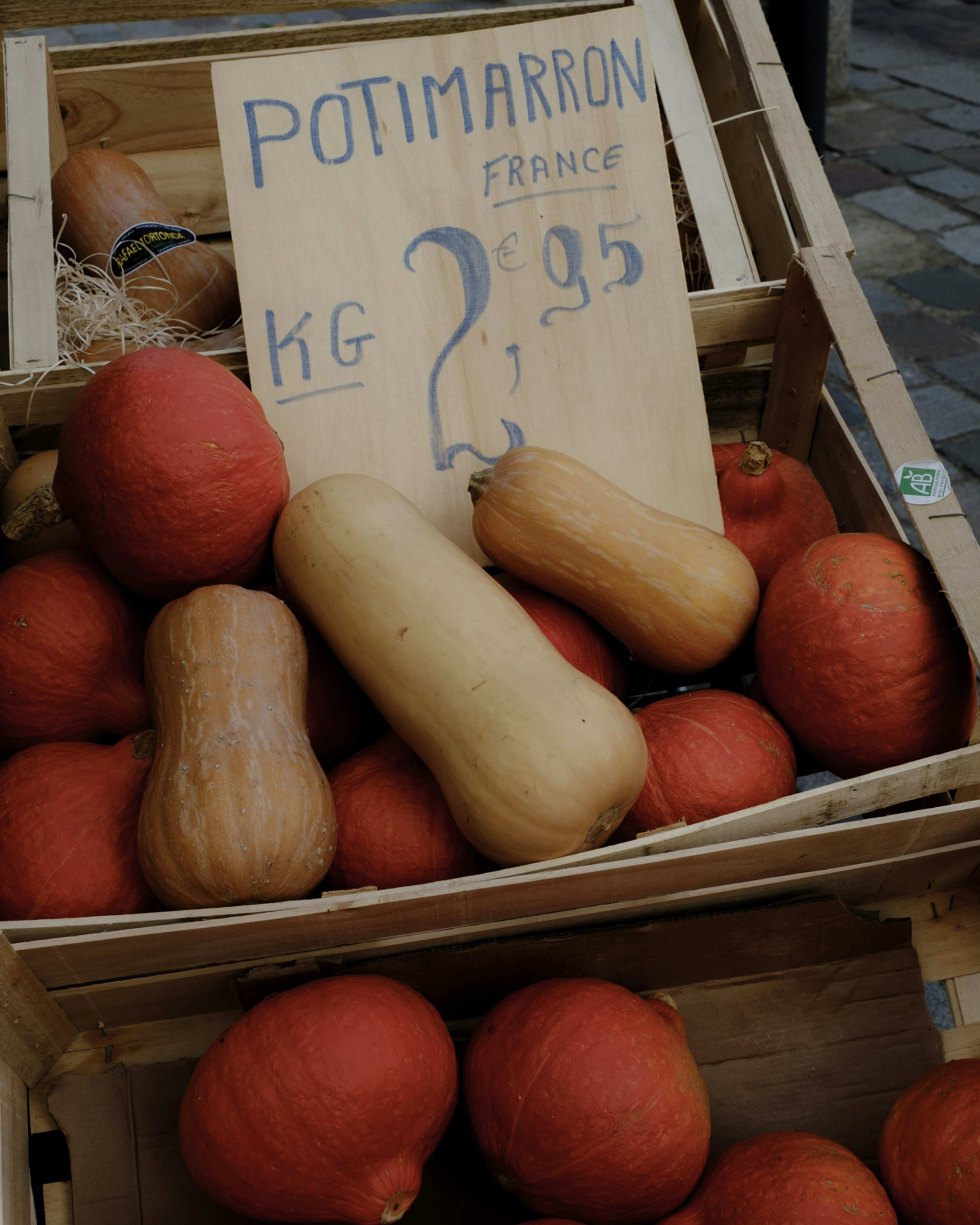 Colorful assortment of pumpkins and squash in a wooden crate, accompanied by a hand-painted price sign. Perfectly captures the essence of a local market.